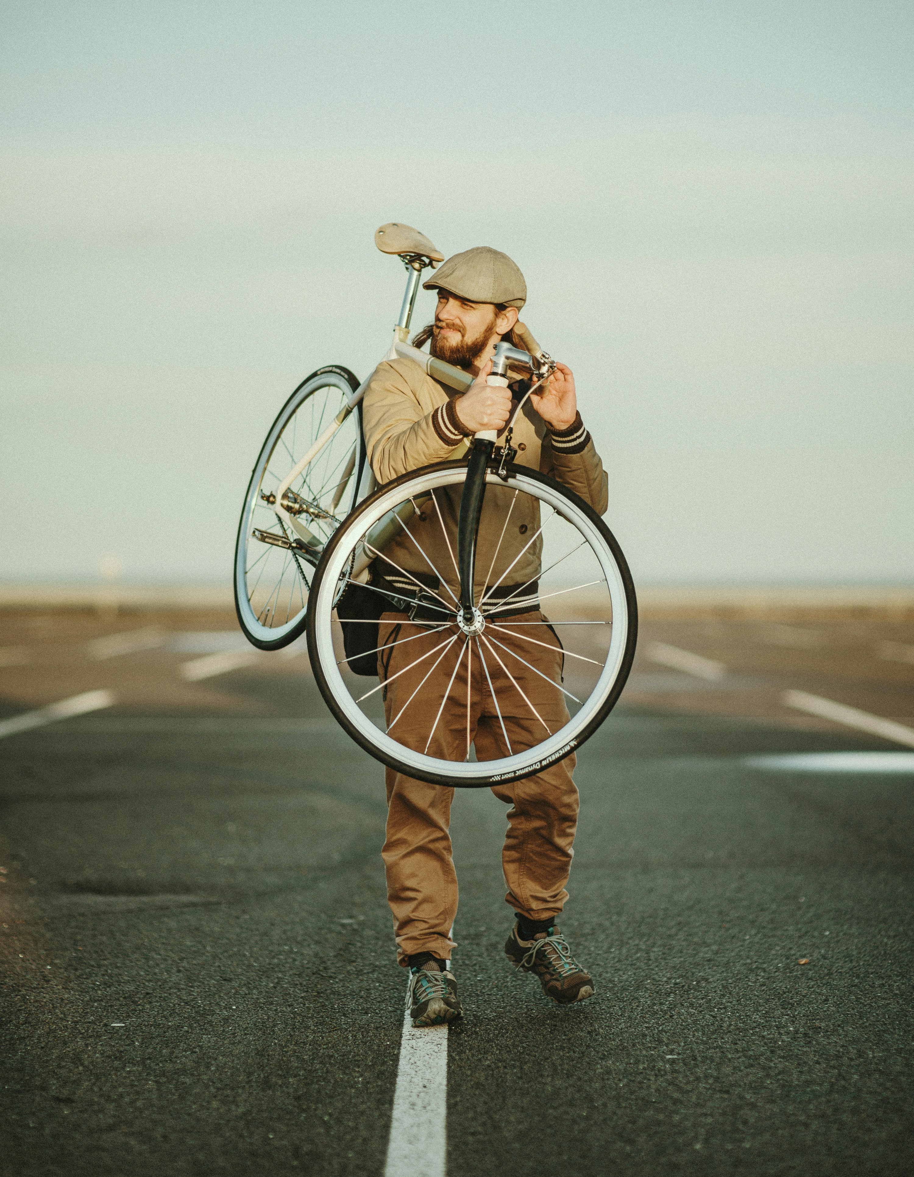 Man carrying a bicycle over his shoulder while standing on an empty road under a clear sky.