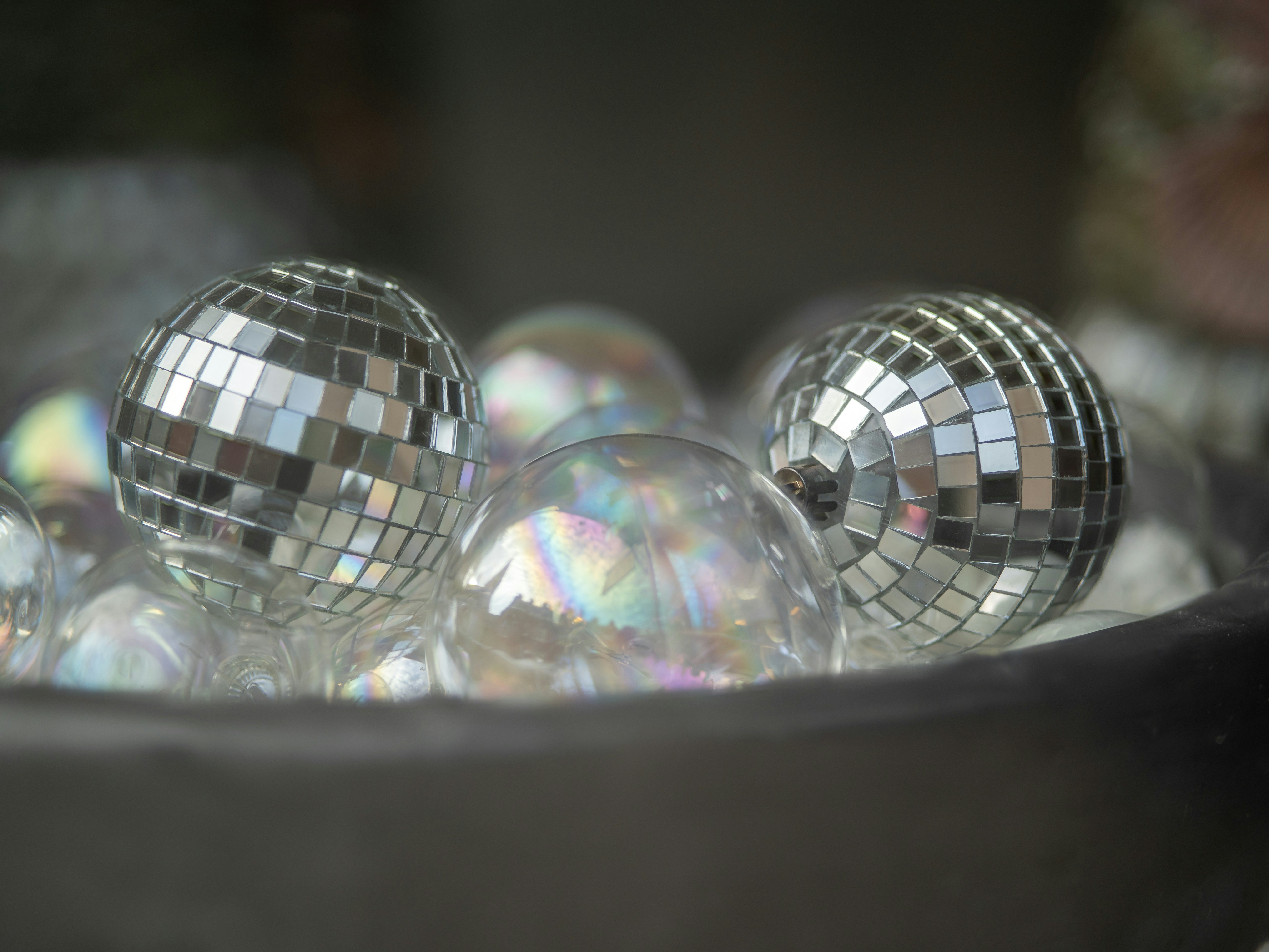 A collection of shimmering disco balls and clear orbs resting in a dark bowl, creating a mesmerizing interplay of reflections and colors.