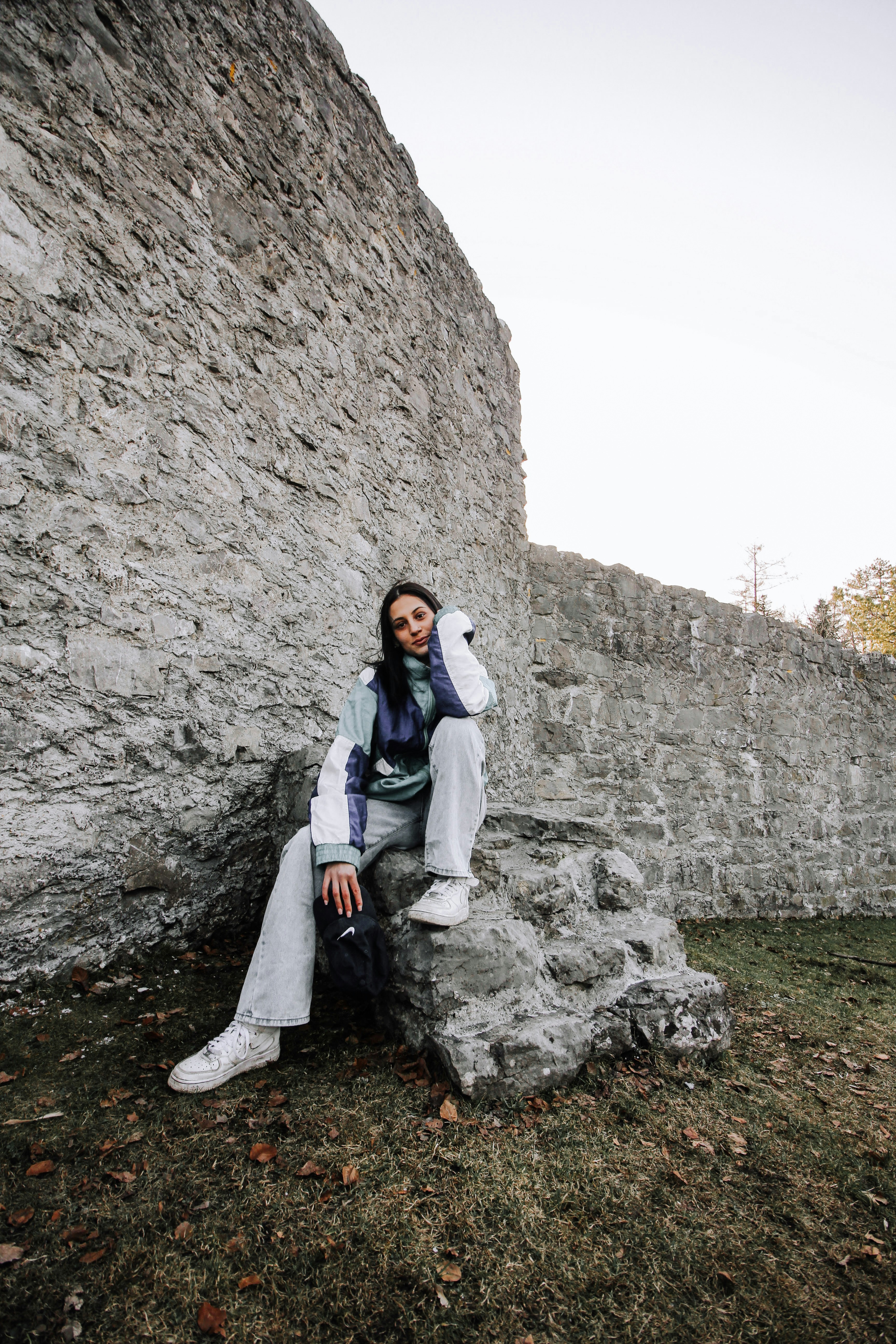 woman in gray jacket sitting on gray rock
