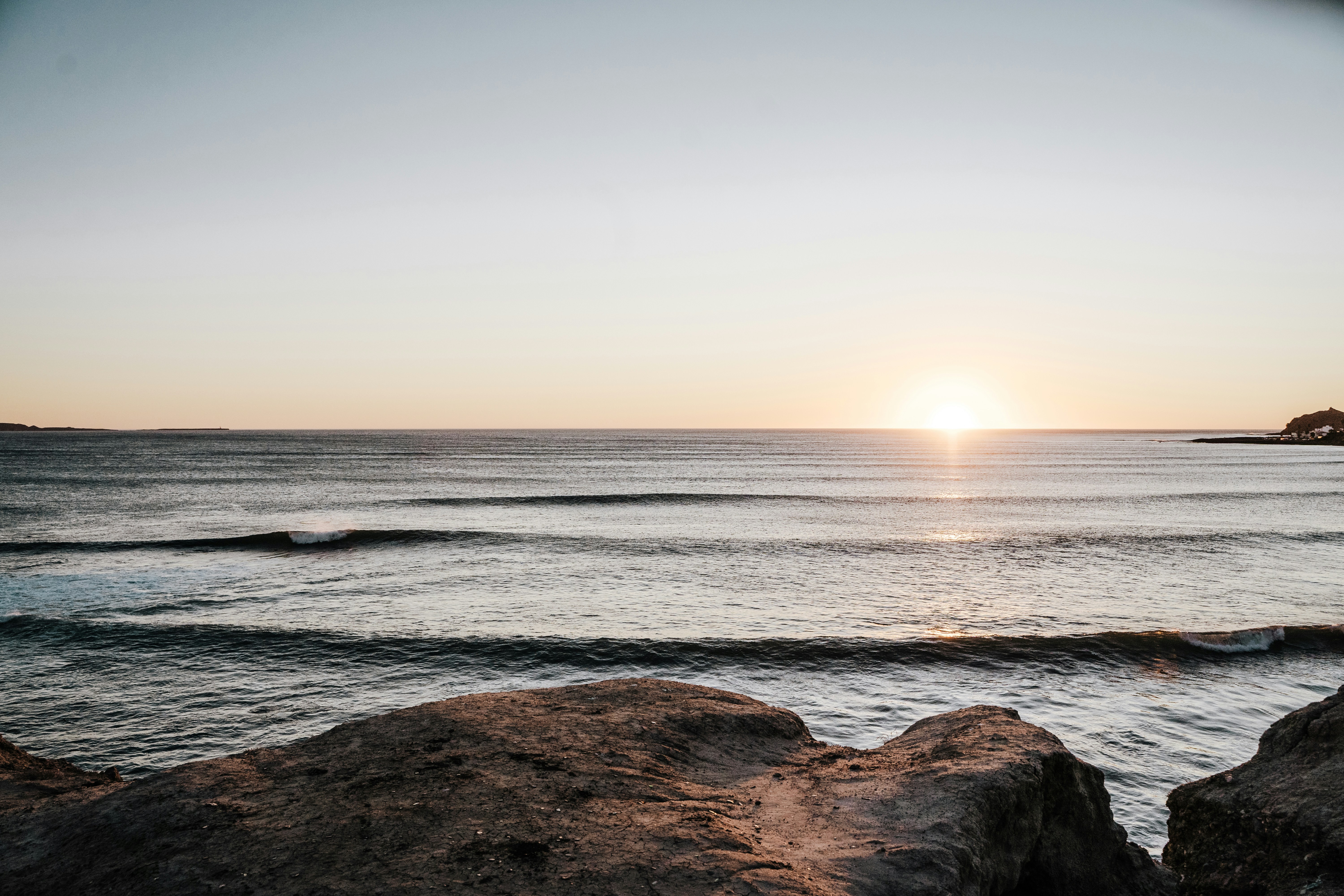 Sunrise over a tranquil ocean with gentle waves lapping against the rocky shore.