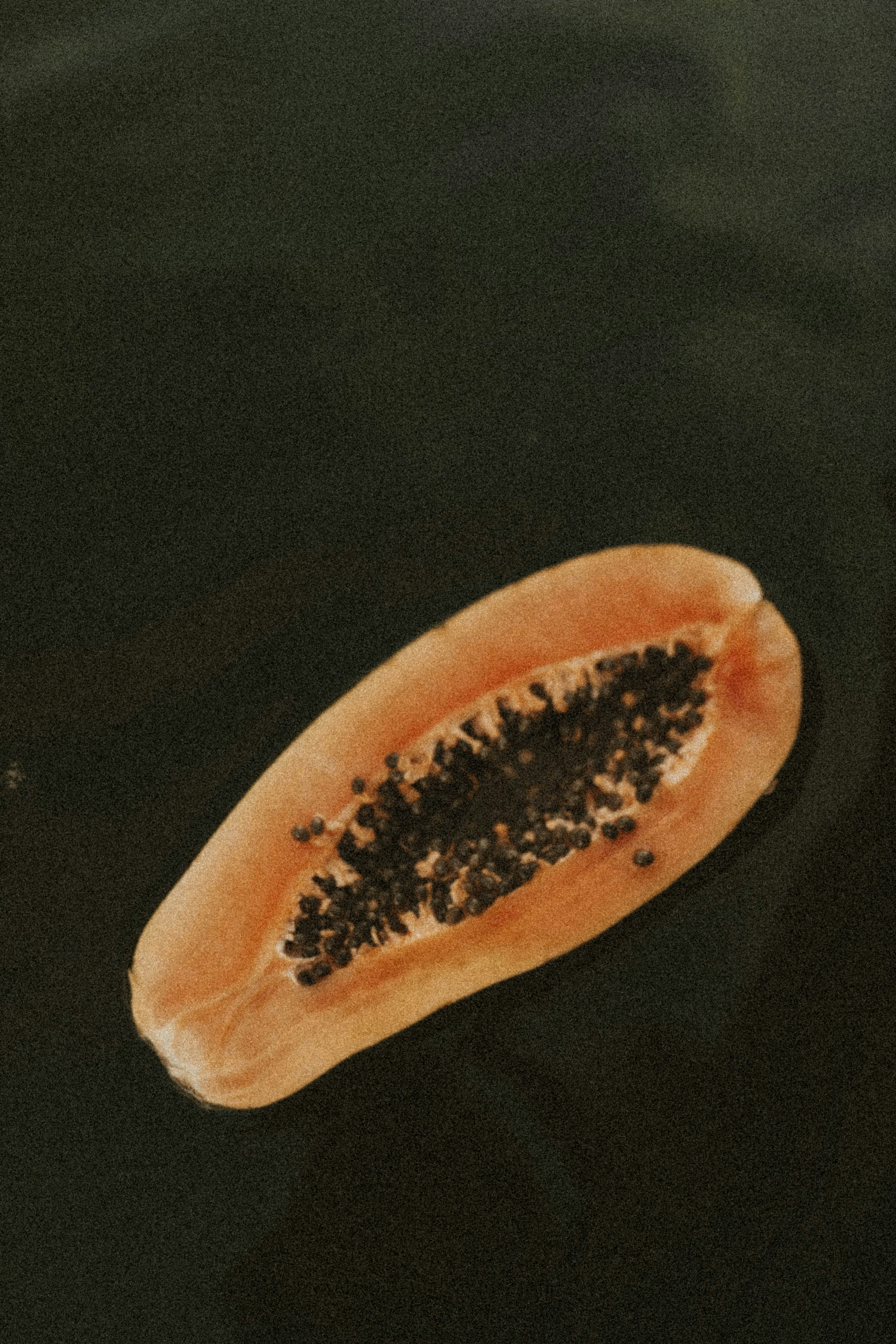 A papaya slice floating gracefully on dark water, showcasing its vibrant orange hue and contrasting black seeds.