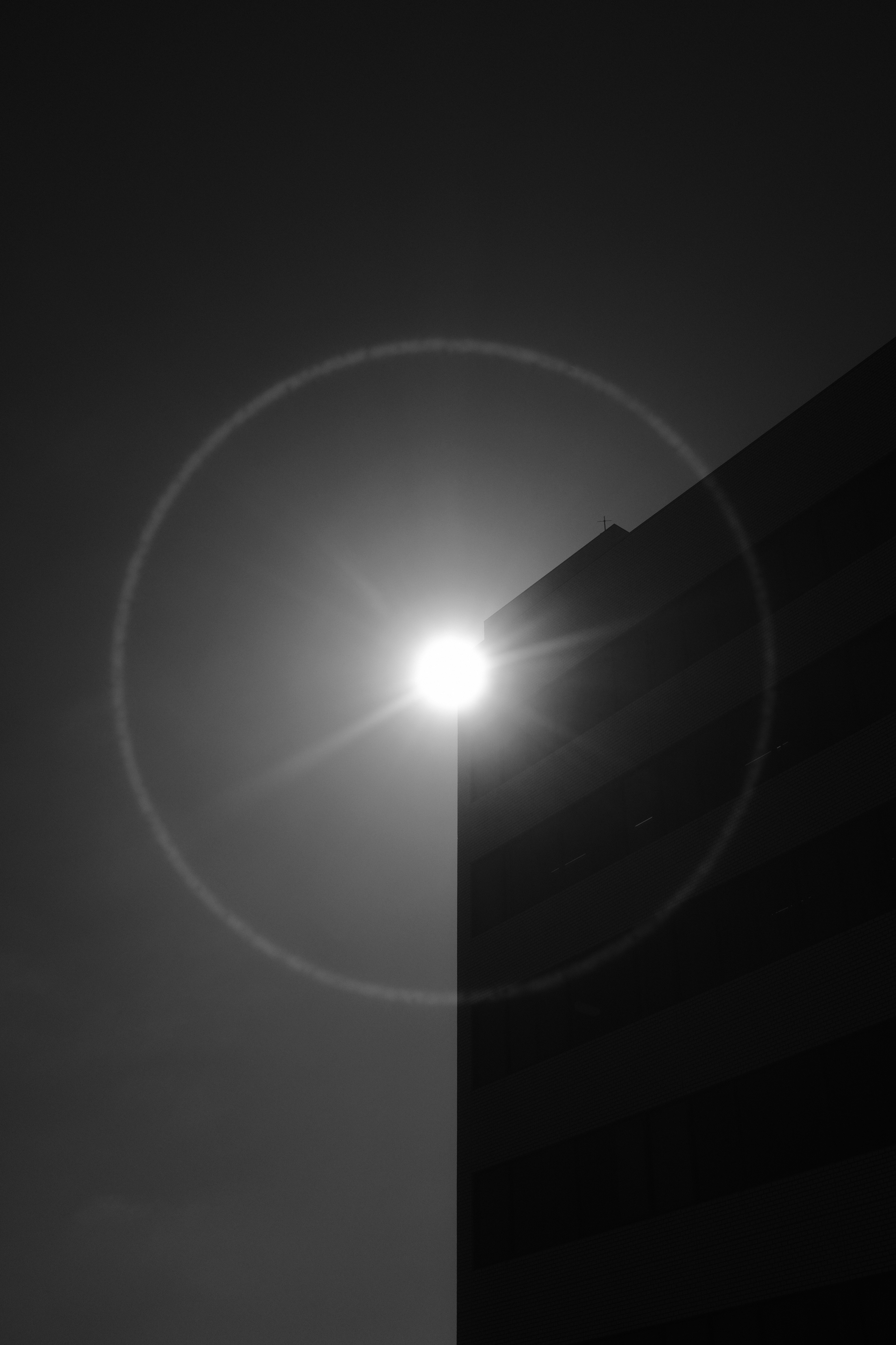 Sunlight creating a halo effect around a building's edge, contrasting with the deep black and white tones of the scene.