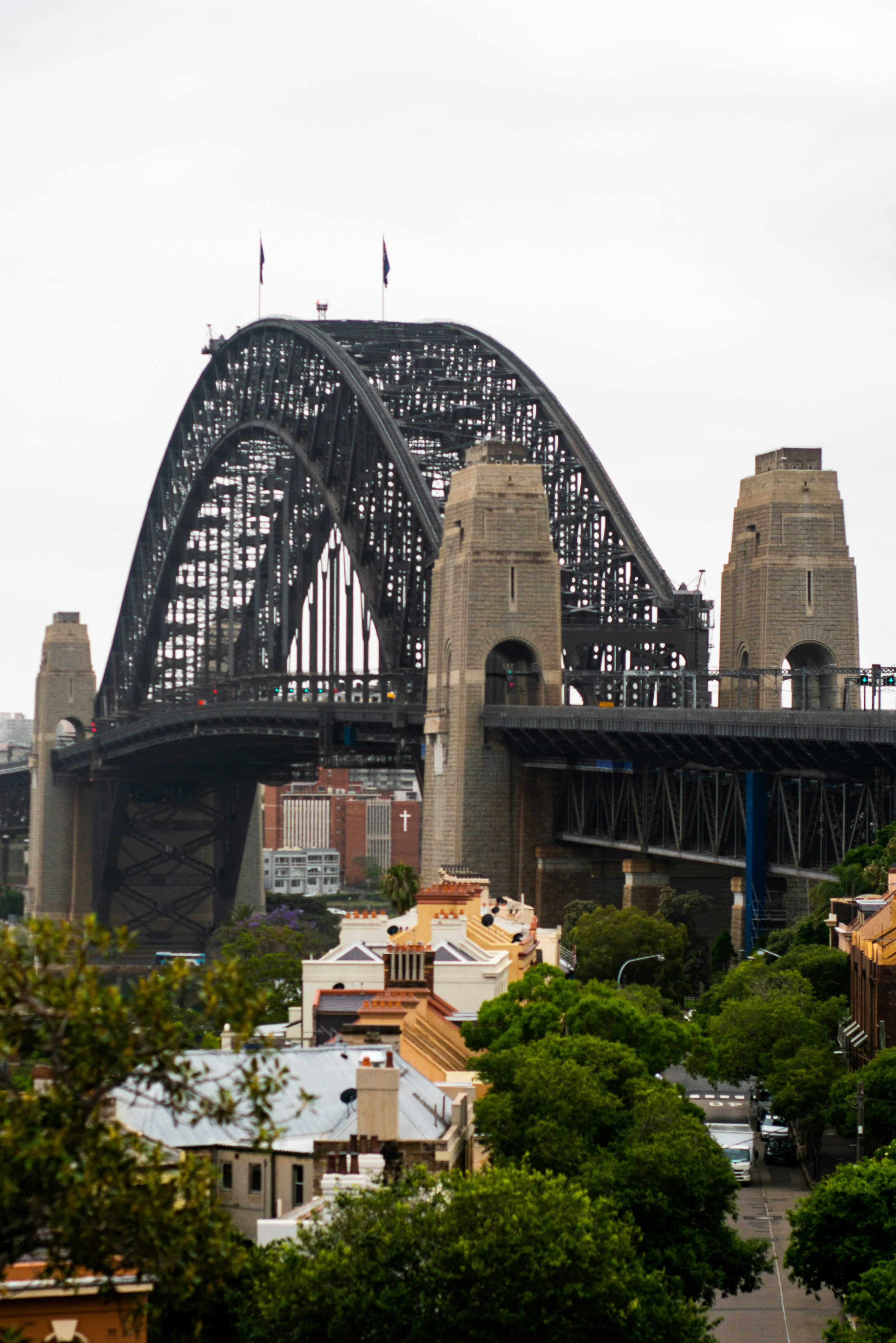 Sydney Harbour Bridge arches gracefully over the cityscape, framed by lush greenery and historic buildings below.