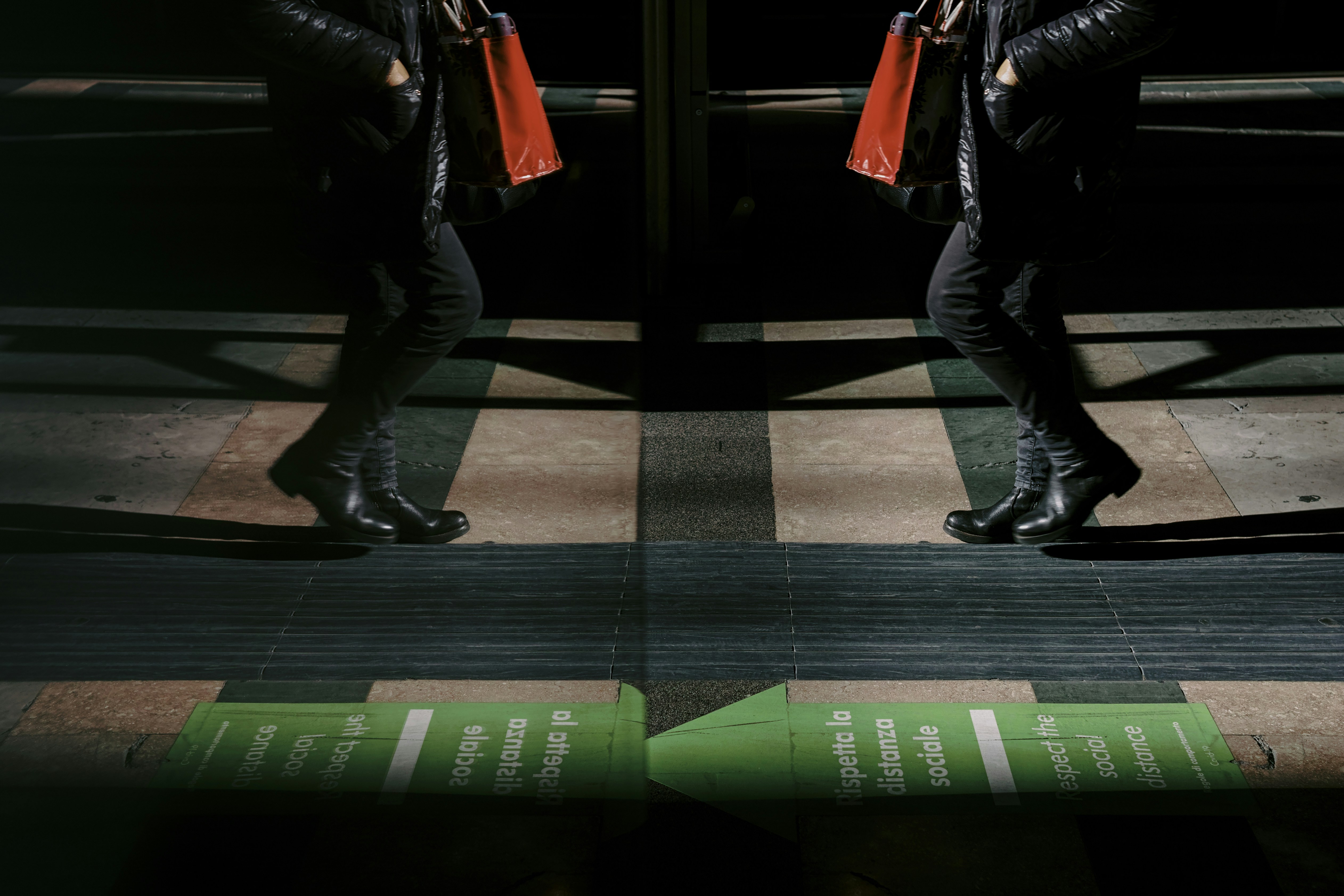 A person walks past illuminated directional signs on a city pavement at night, creating a striking contrast between shadows and light.