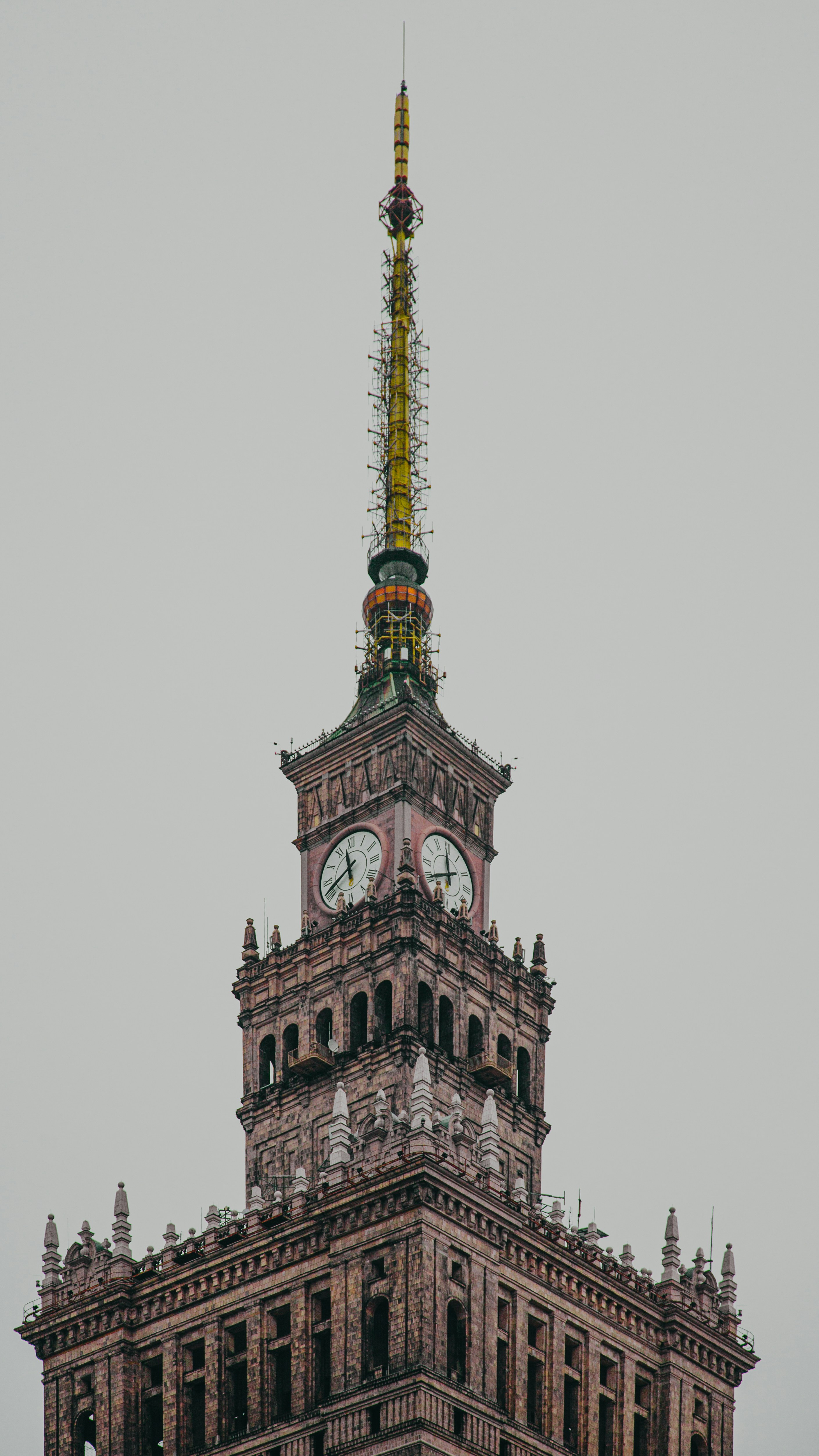 Clock tower adorned with intricate detailing and a vibrant spire, rising against a muted sky.