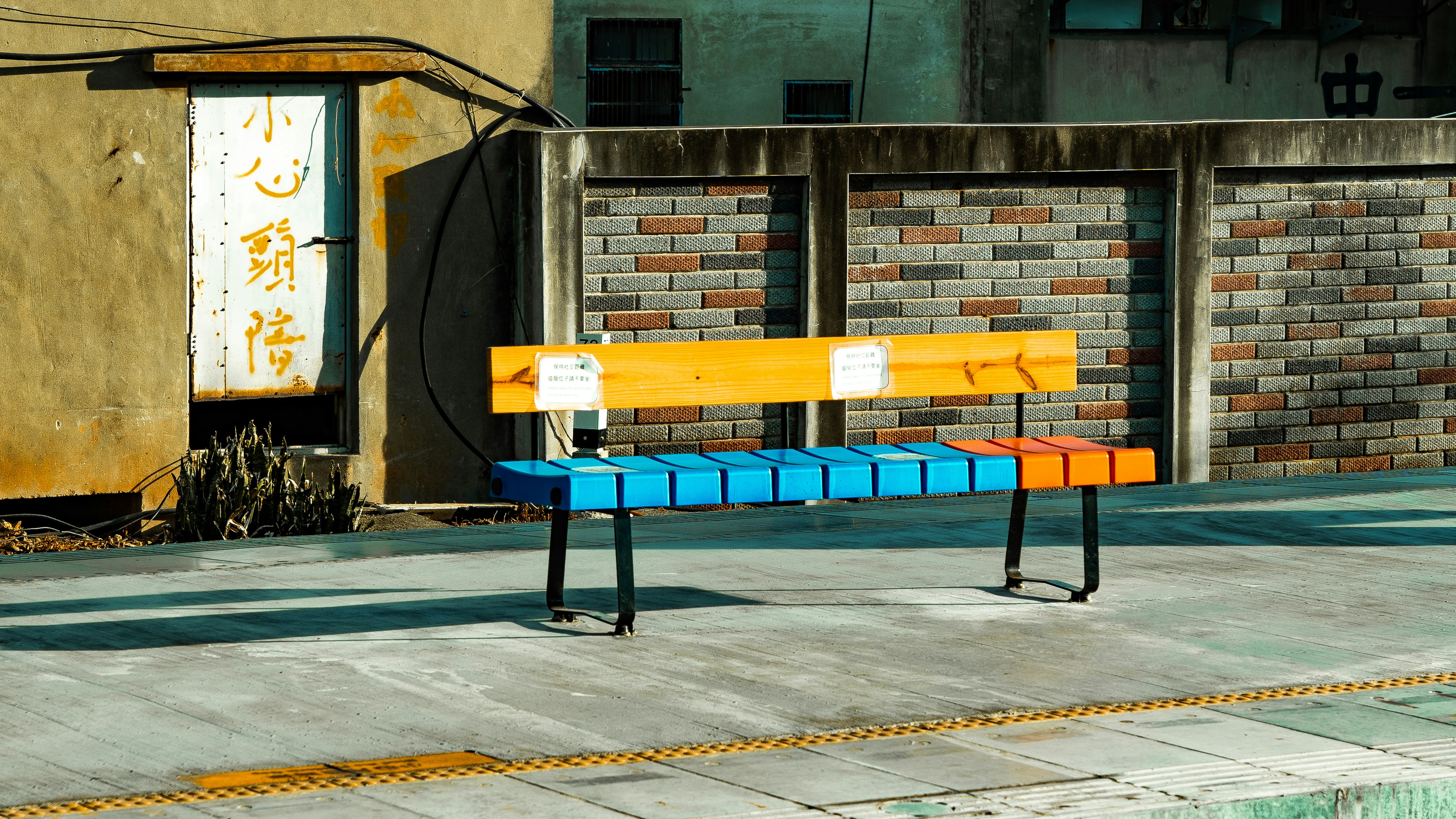 Colorful bench on a sunlit urban sidewalk beside a textured wall.