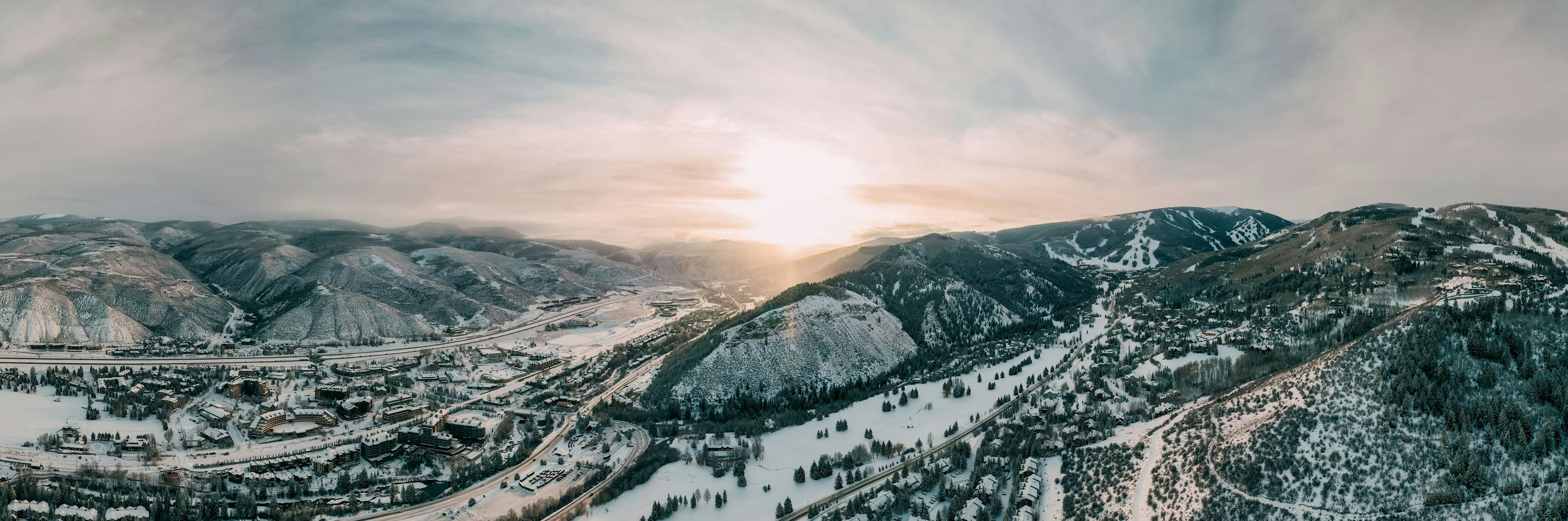 Panoramic view of a snow-covered valley at sunset, showcasing rolling hills and a quiet town nestled in the landscape.
