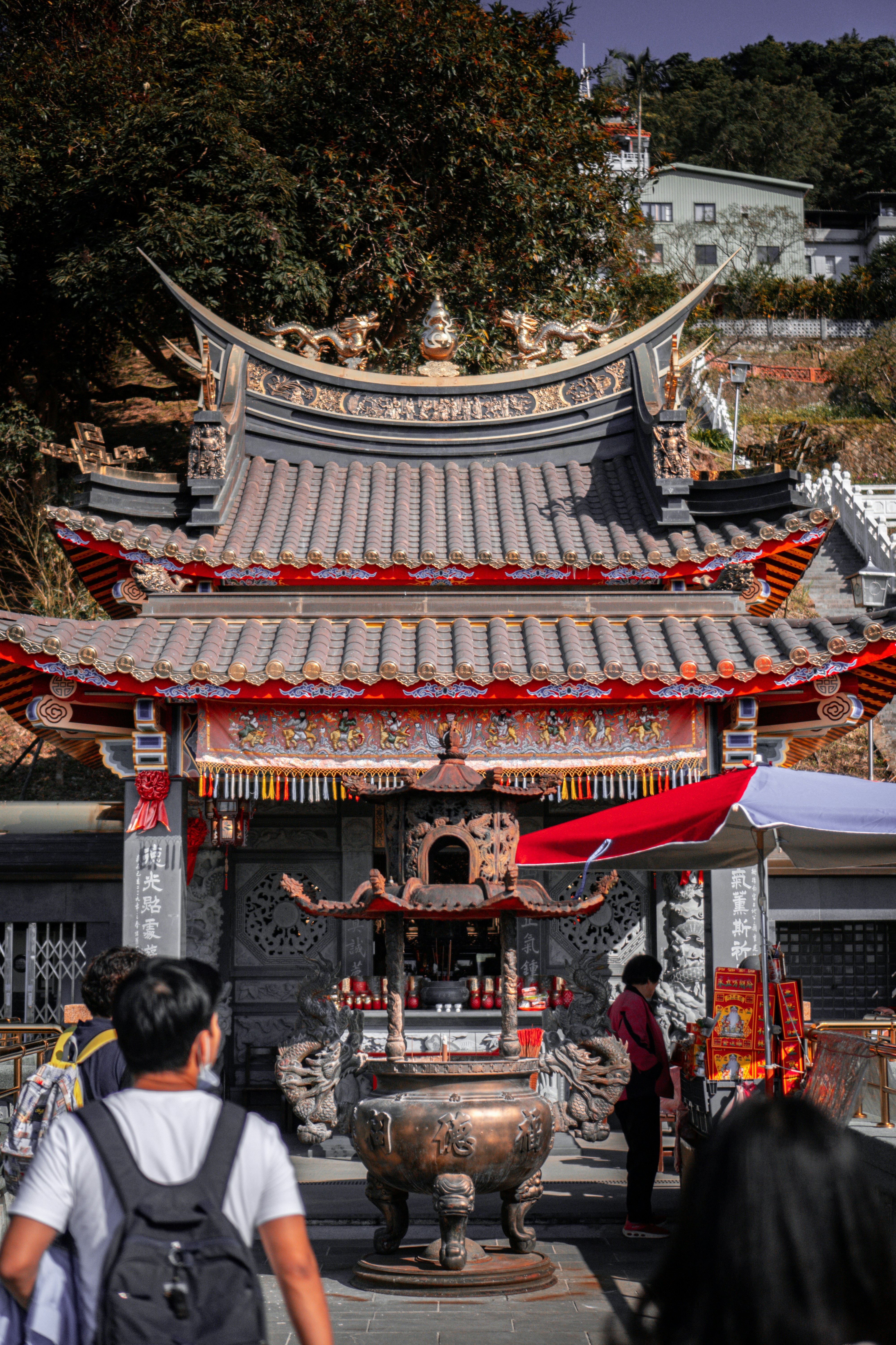 Intricate temple structure adorned with vibrant decorations, featuring a central incense burner surrounded by visitors in a bustling atmosphere.
