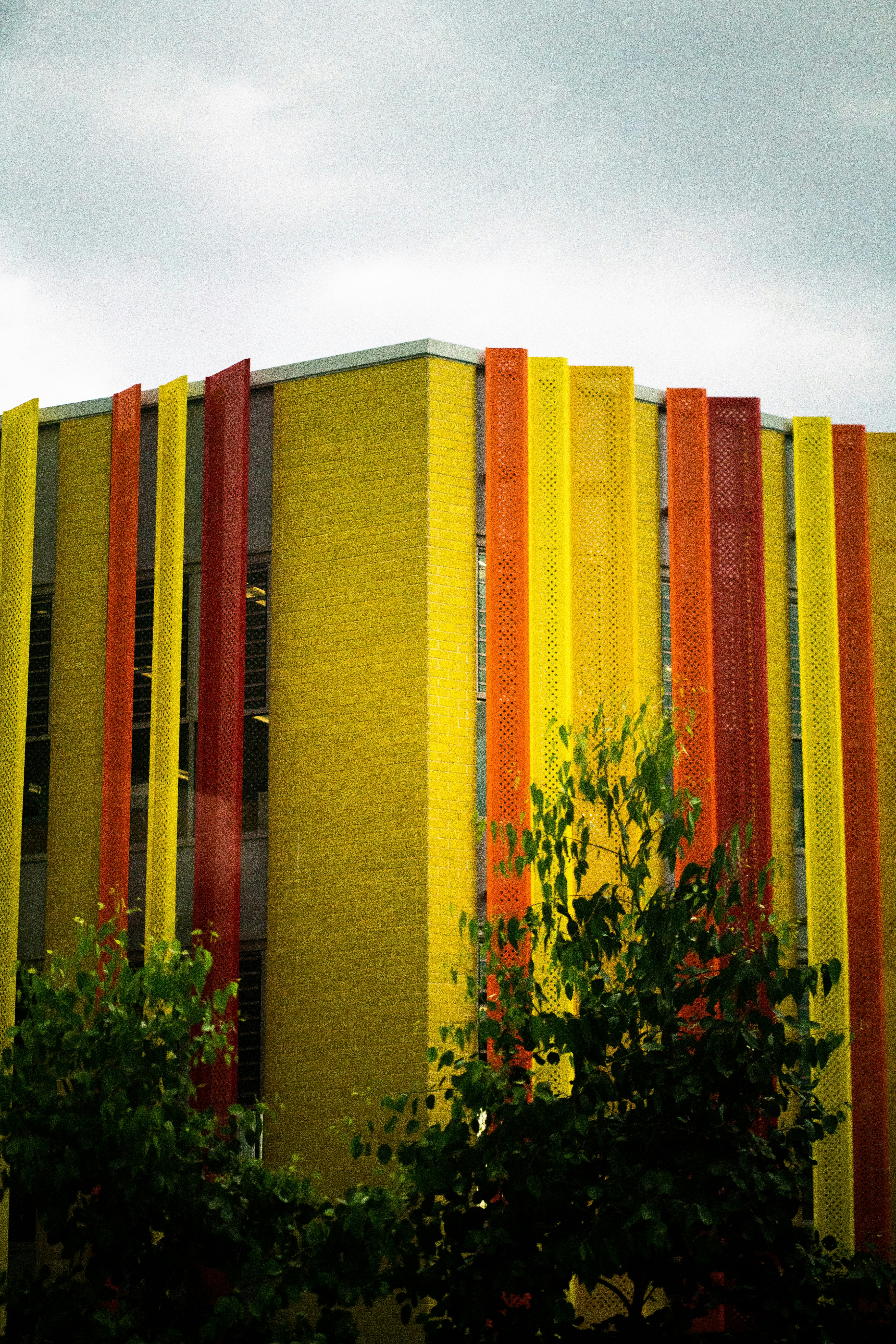 Vibrant facade of a modern building featuring bold vertical stripes in yellow, red, and orange, contrasted by lush greenery below.