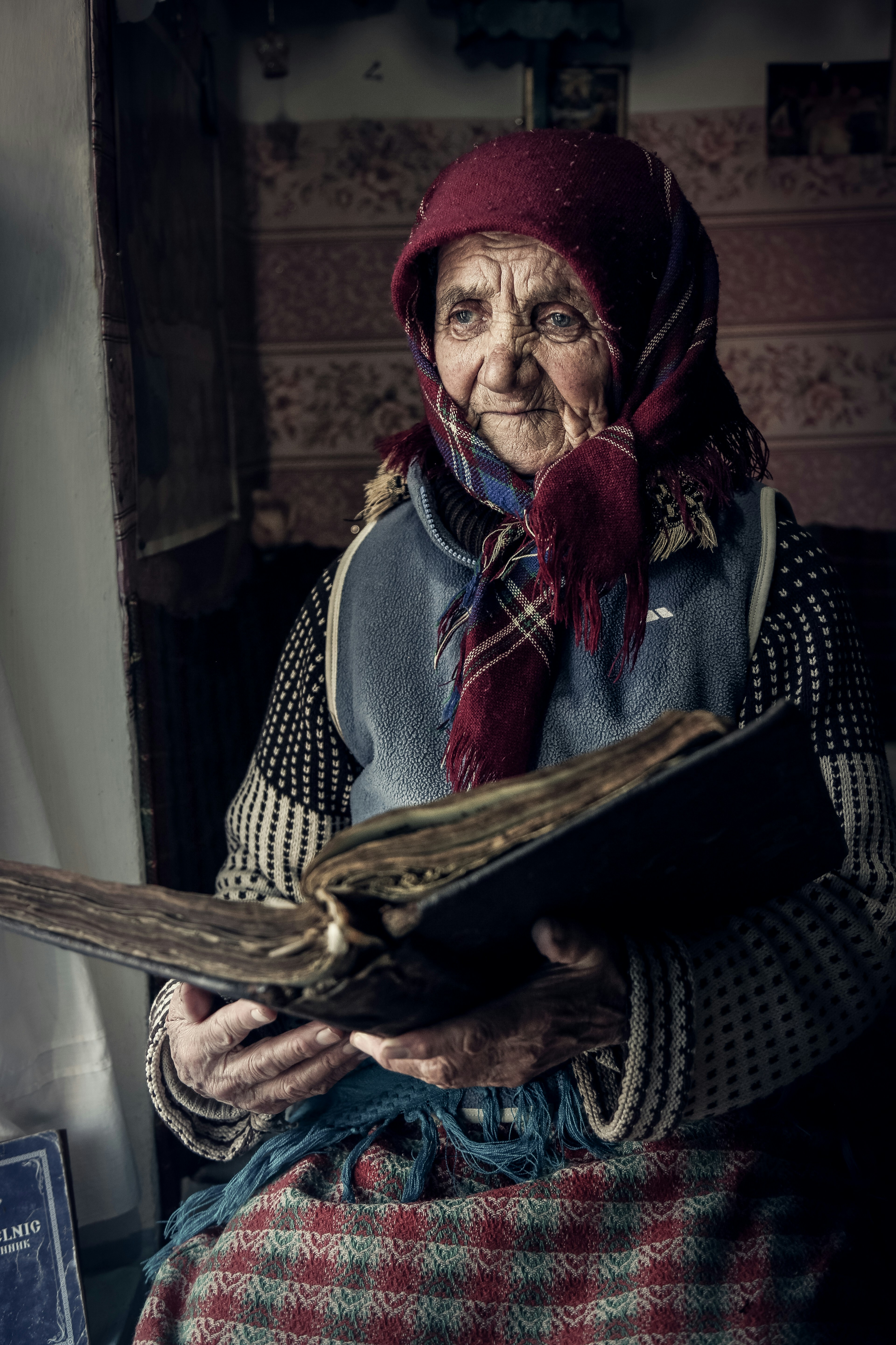 Elderly woman holding an ancient book, embodying a rich history and tradition. Natural light illuminates her thoughtful expression.