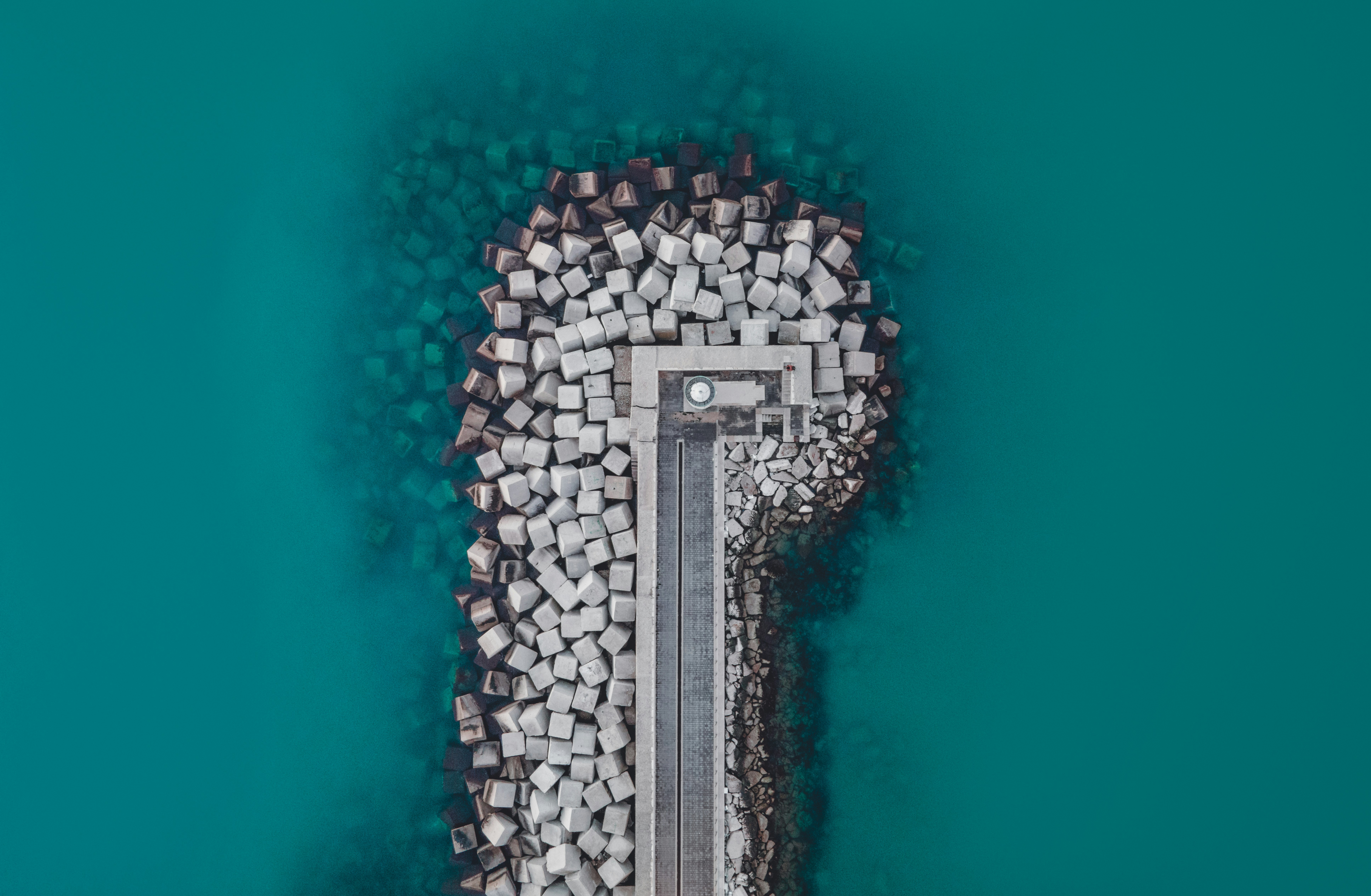 Drone view of a jetty extending into a sea of turquoise, surrounded by neatly arranged boulders.