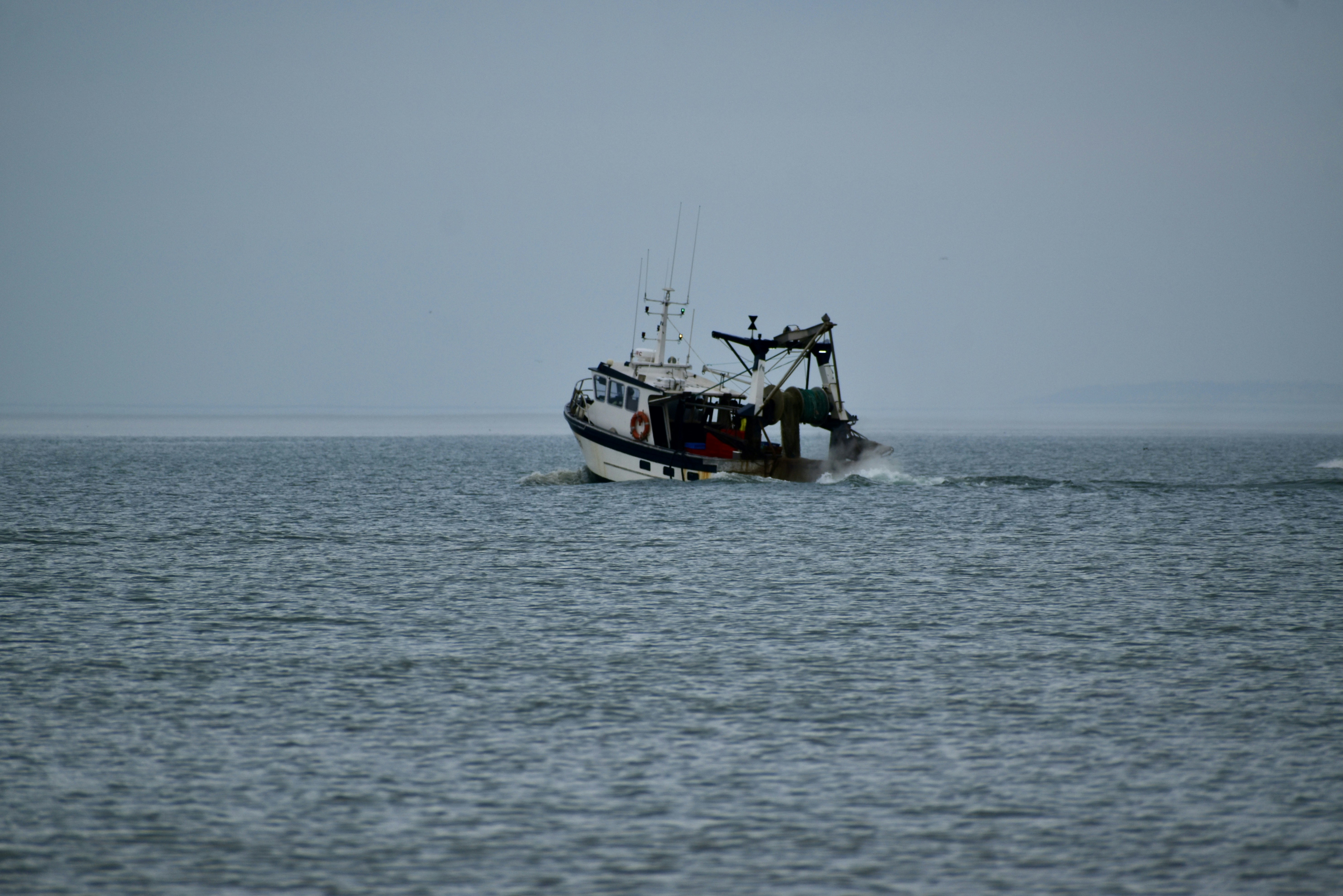 White and black boat cruising on a calm sea under a cloudy sky.