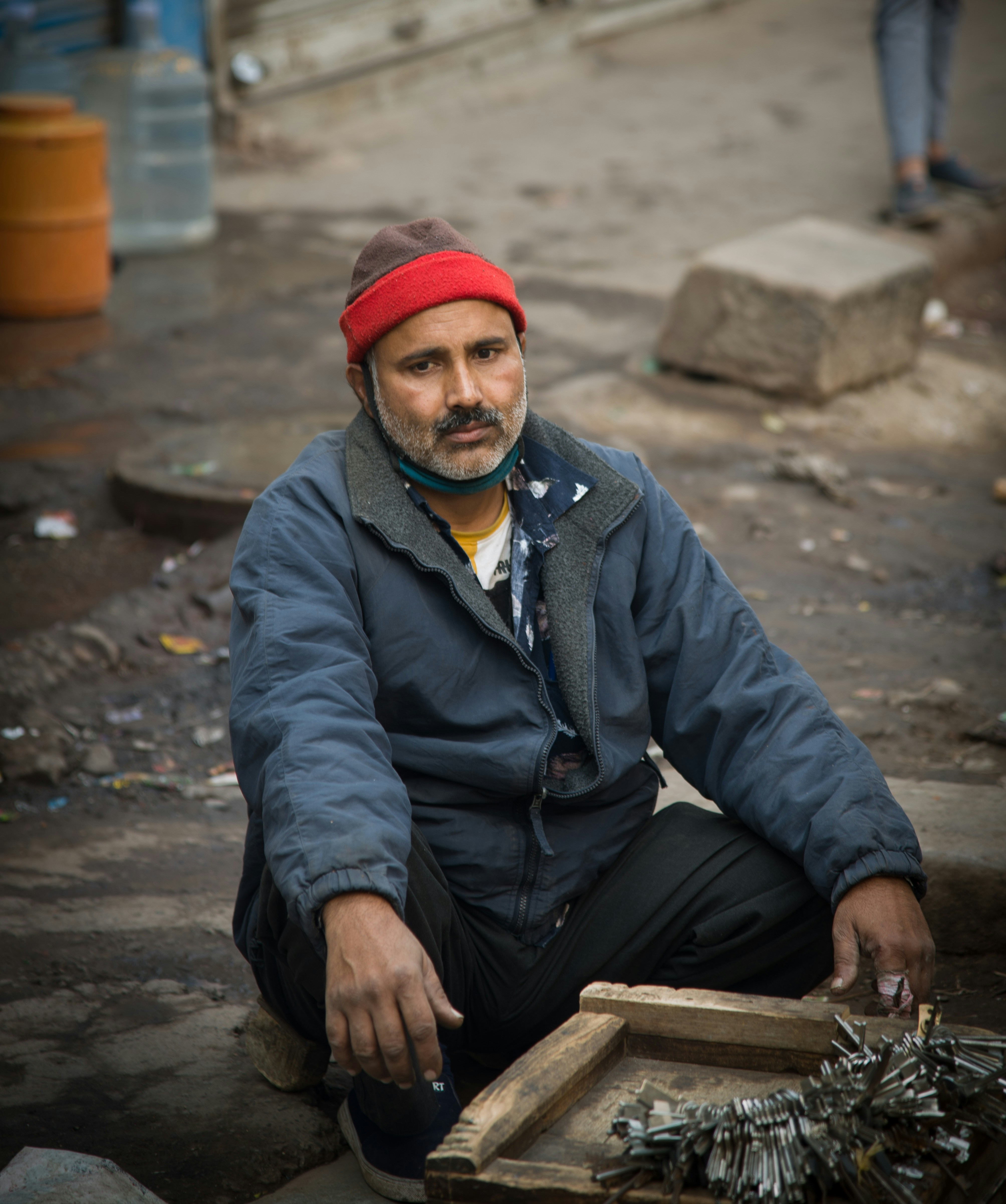 A man seated on the street, focused on a wooden box filled with keys, showcasing the essence of craftsmanship in an urban setting.