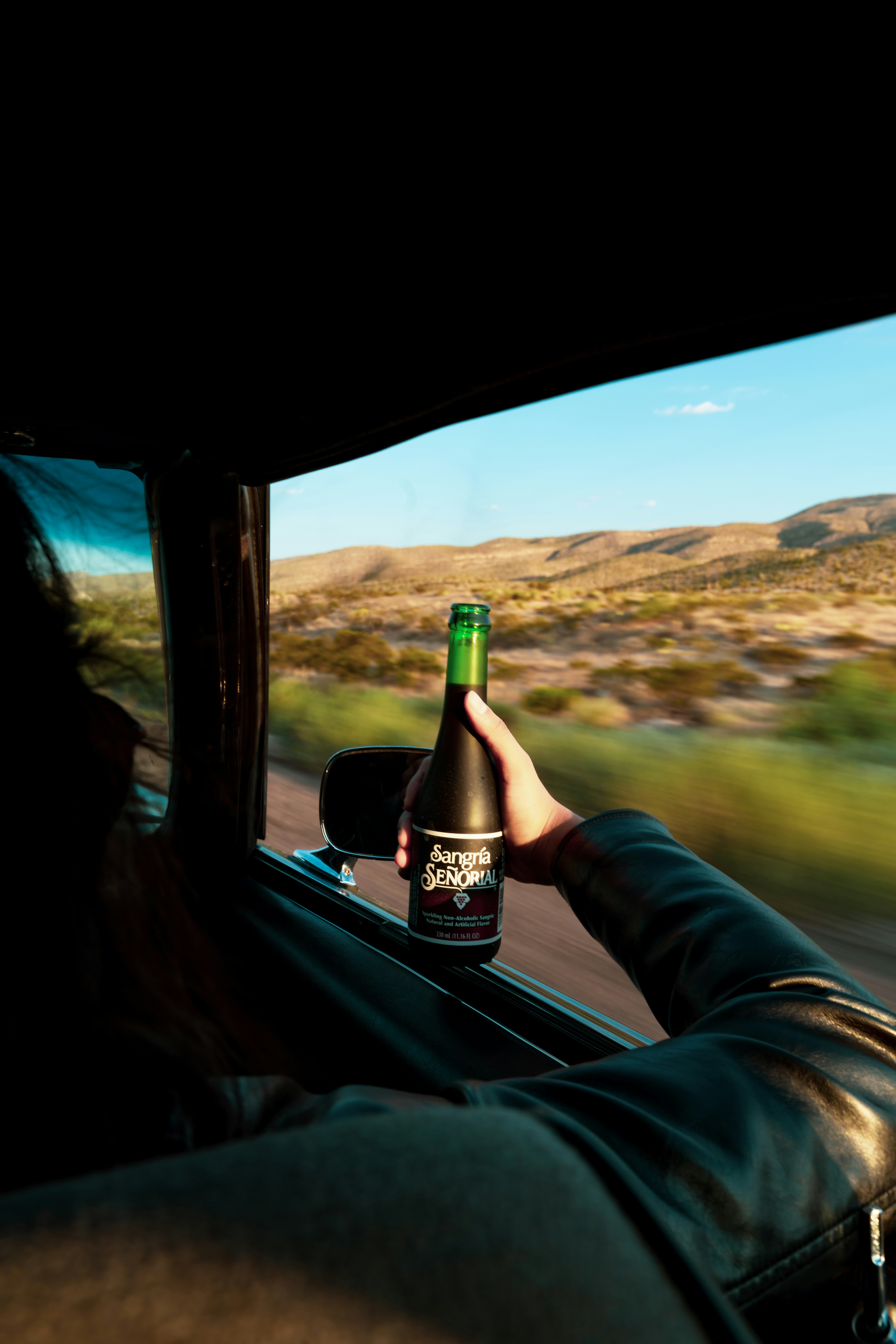 Rolling Desert Toast: A Green Bottle Framed by a Car Window