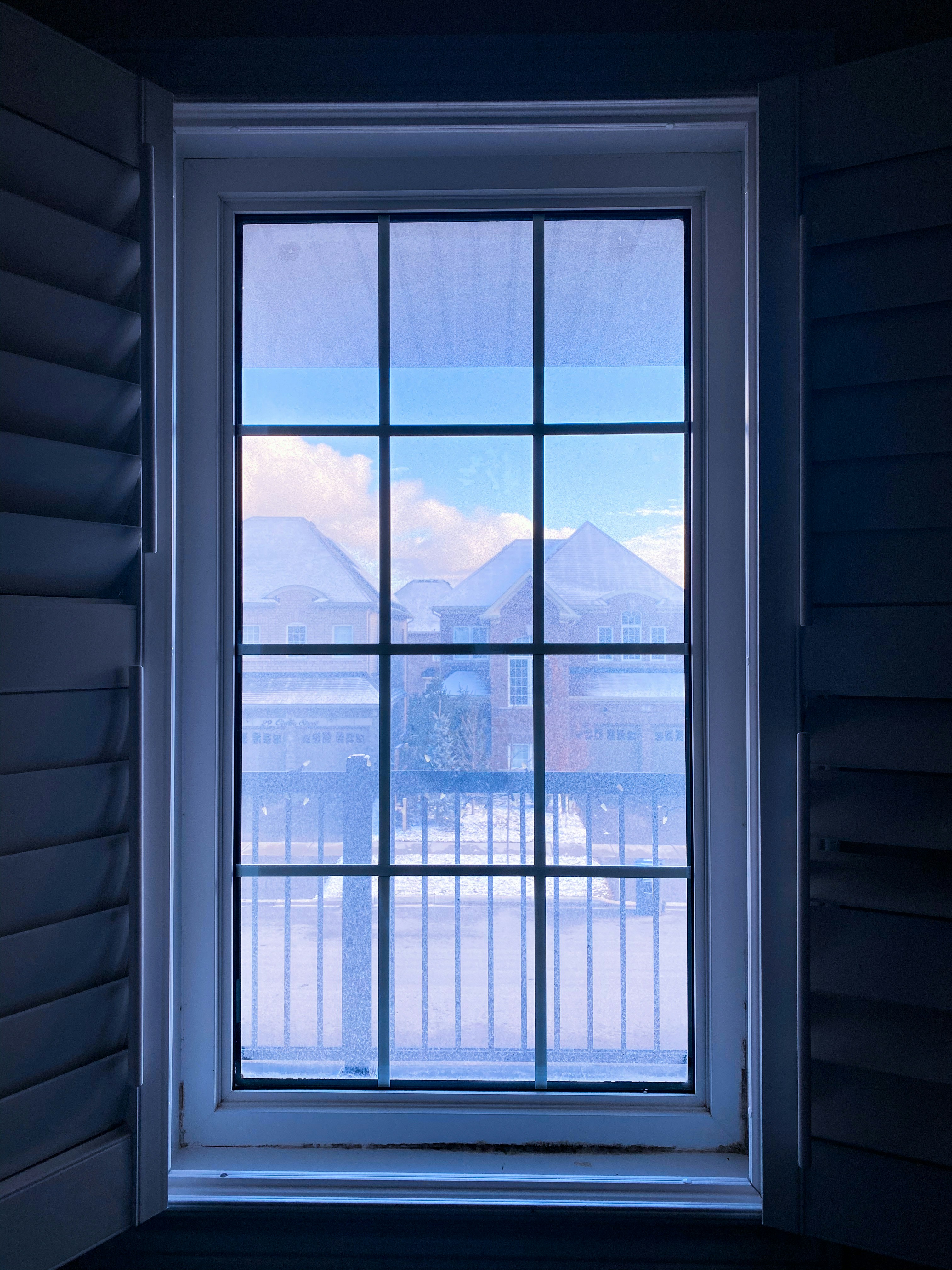 Snow-covered houses viewed through a window with a grid pattern, capturing a tranquil winter scene.