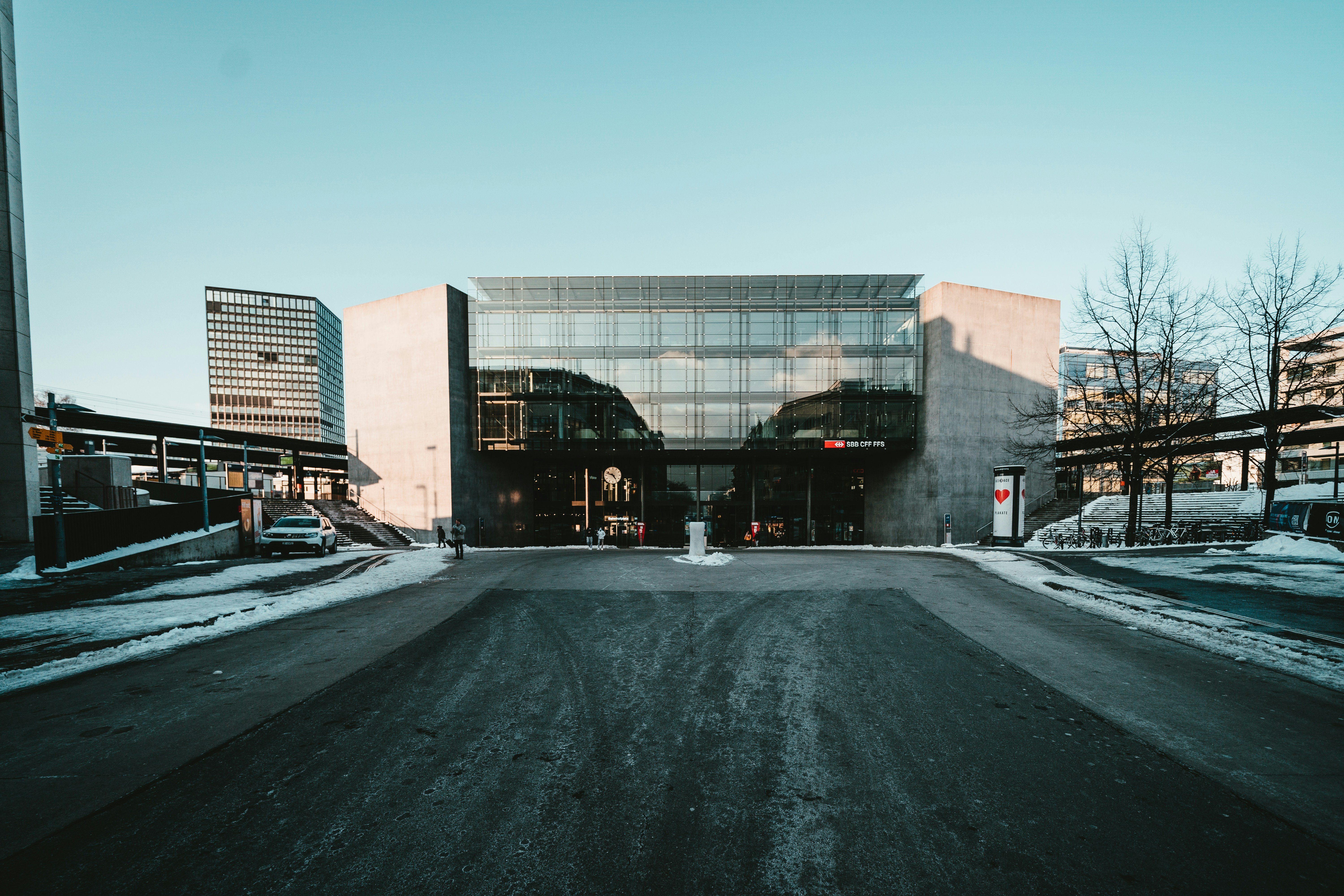 Modern building with a glass facade reflecting the blue sky, surrounded by snow-covered urban landscape.
