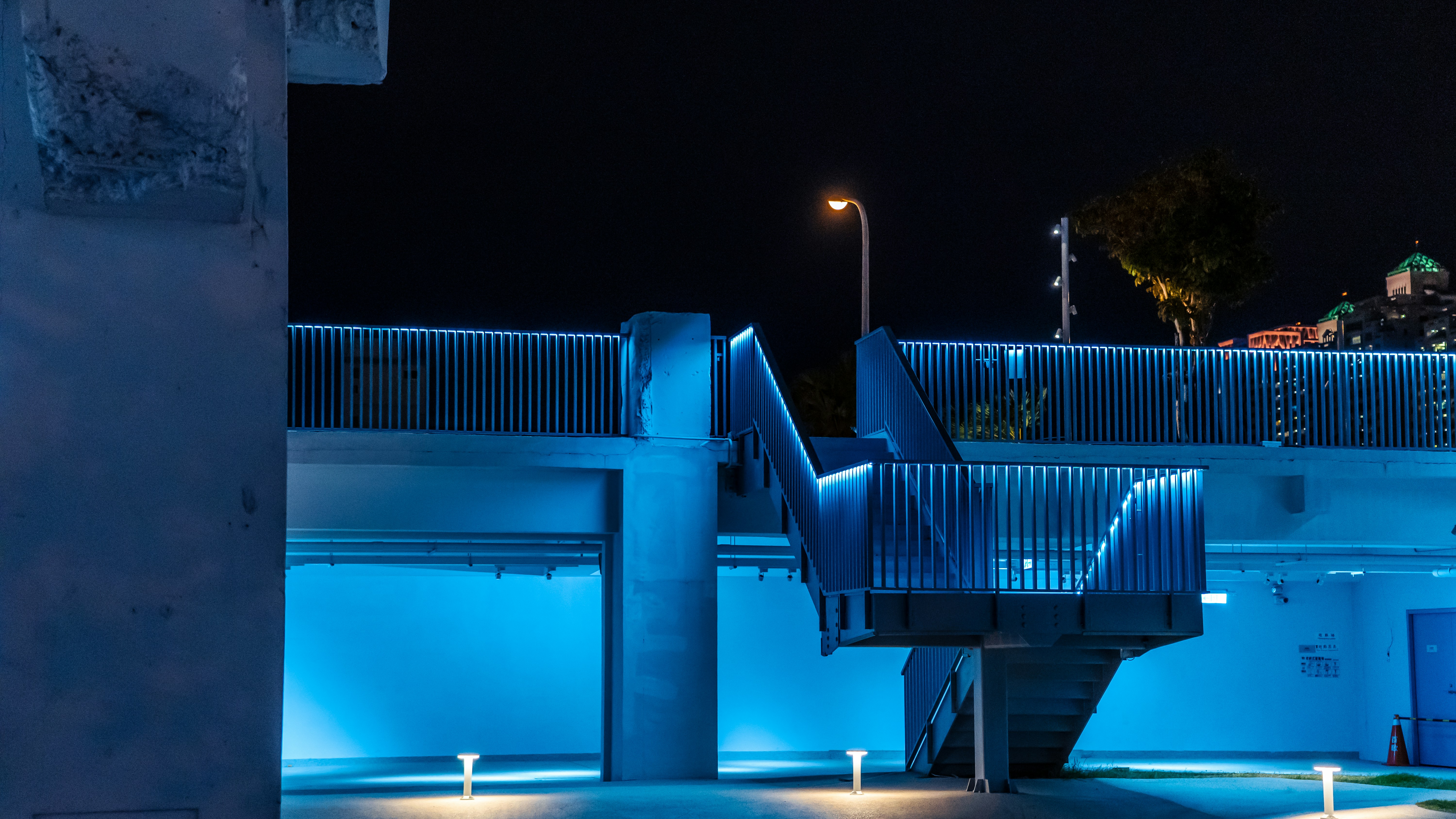 Vibrant blue lighting illuminates a contemporary architectural structure at night, highlighting the interplay of shadows and angles.