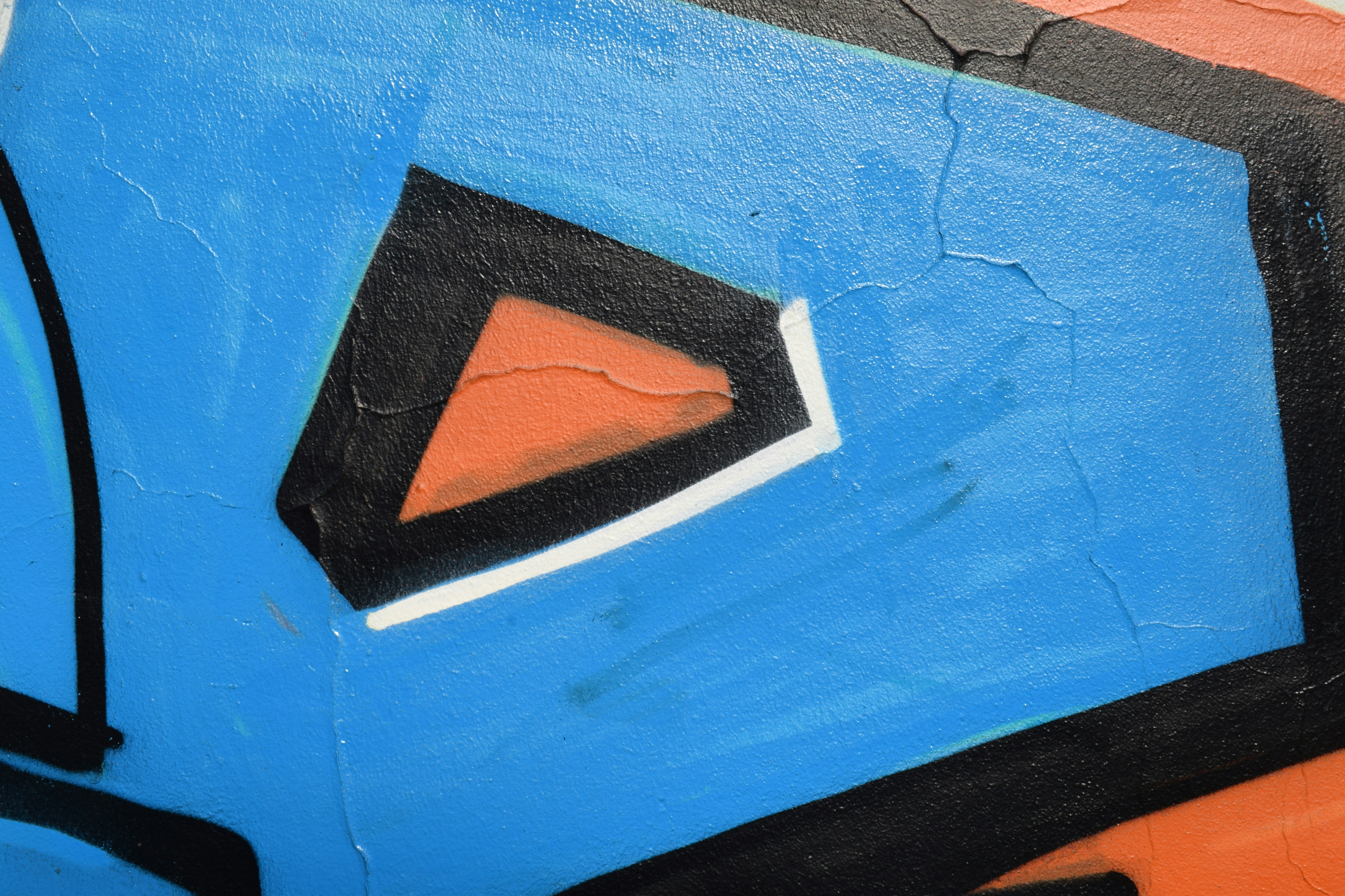 Blue Wall Glyph: Orange Triangle Framed by Black Geometry on a Weathered Azure Surface