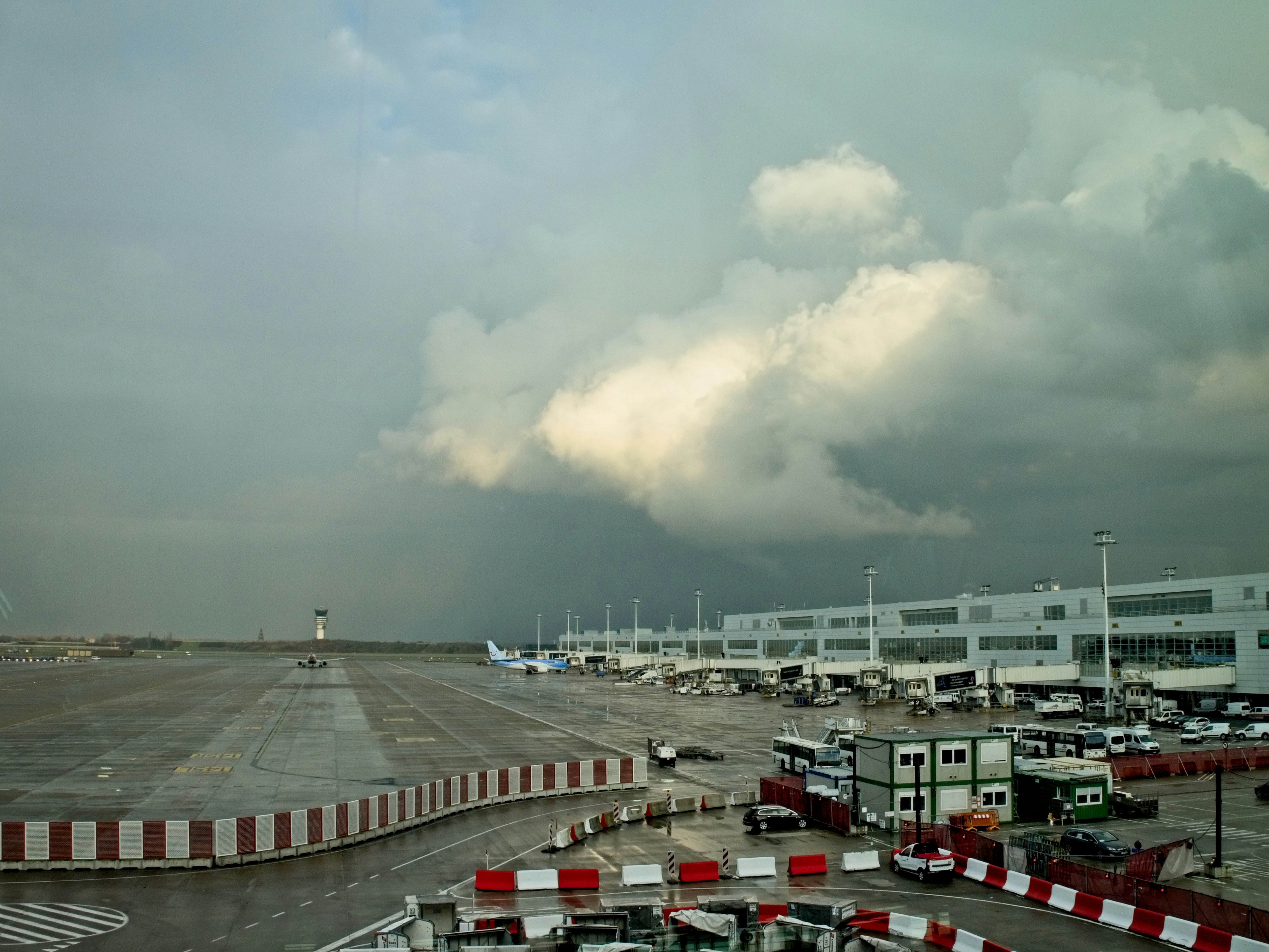 Expansive airport runway under a moody sky, with aircraft and service vehicles parked nearby. The scene evokes a sense of anticipation.
