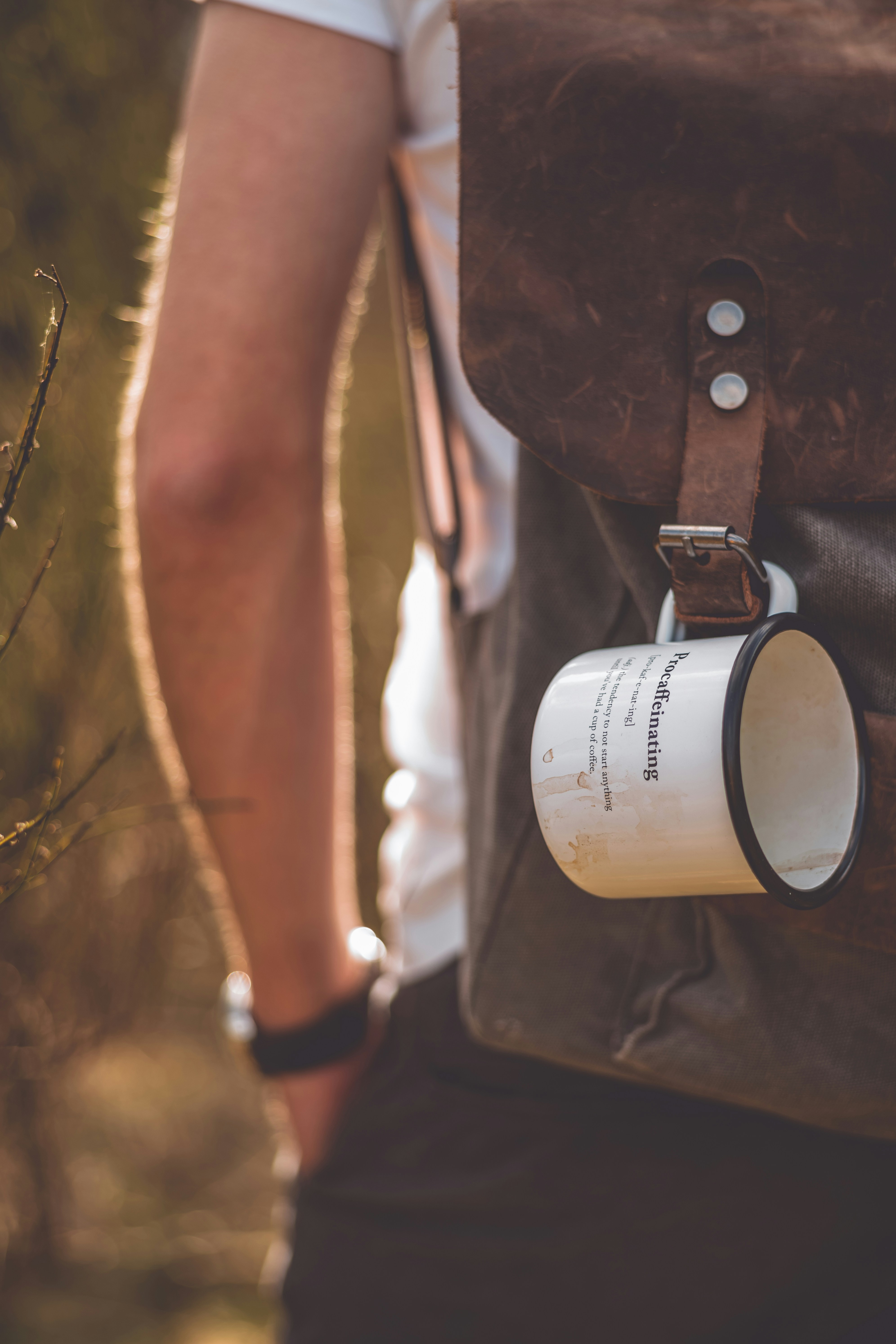 Sunlit Trek: A White Enamel Mug on a Weathered Leather Pack