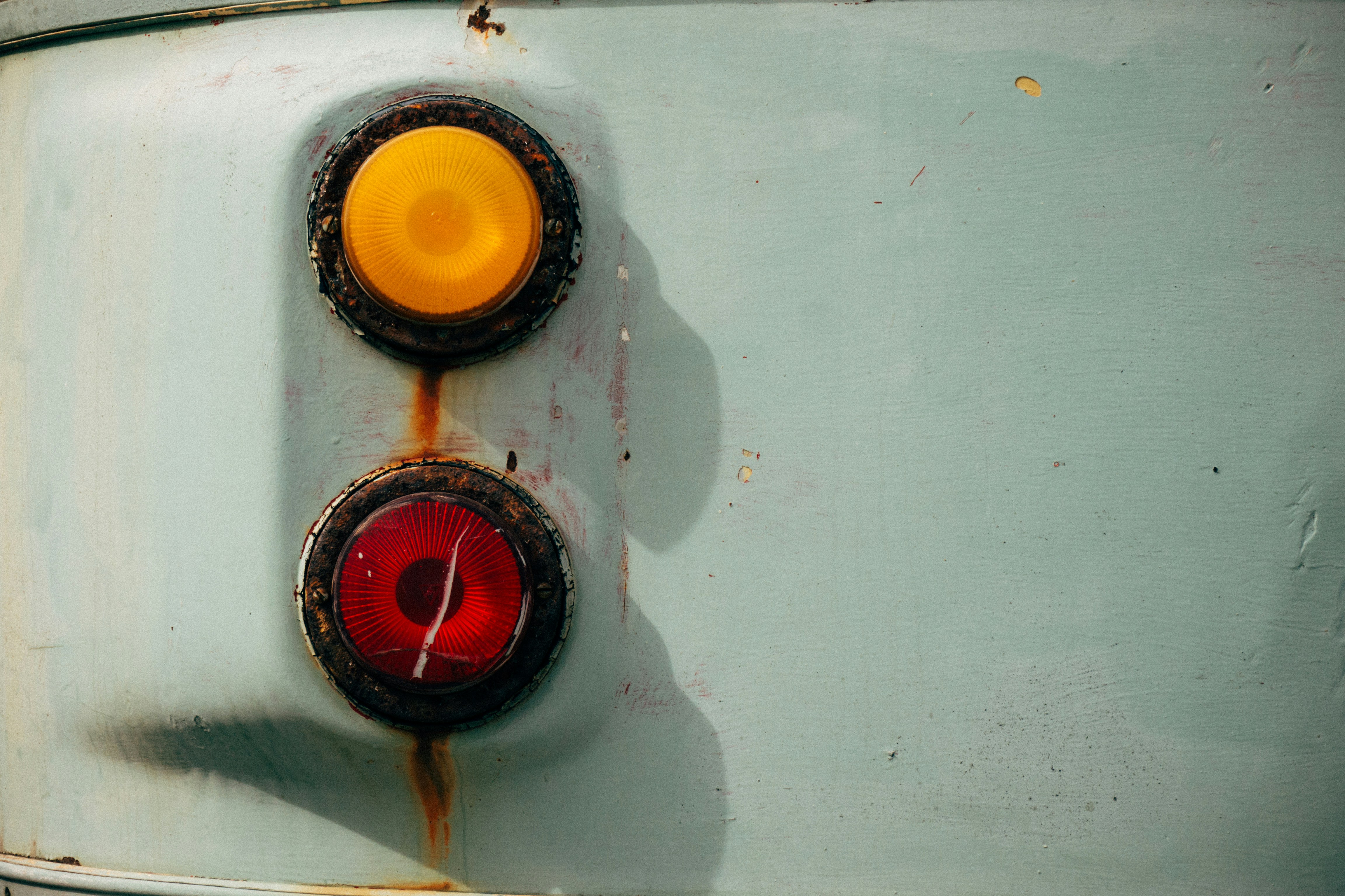 Close-up of vintage vehicle lights featuring a yellow and red light against a weathered blue background.