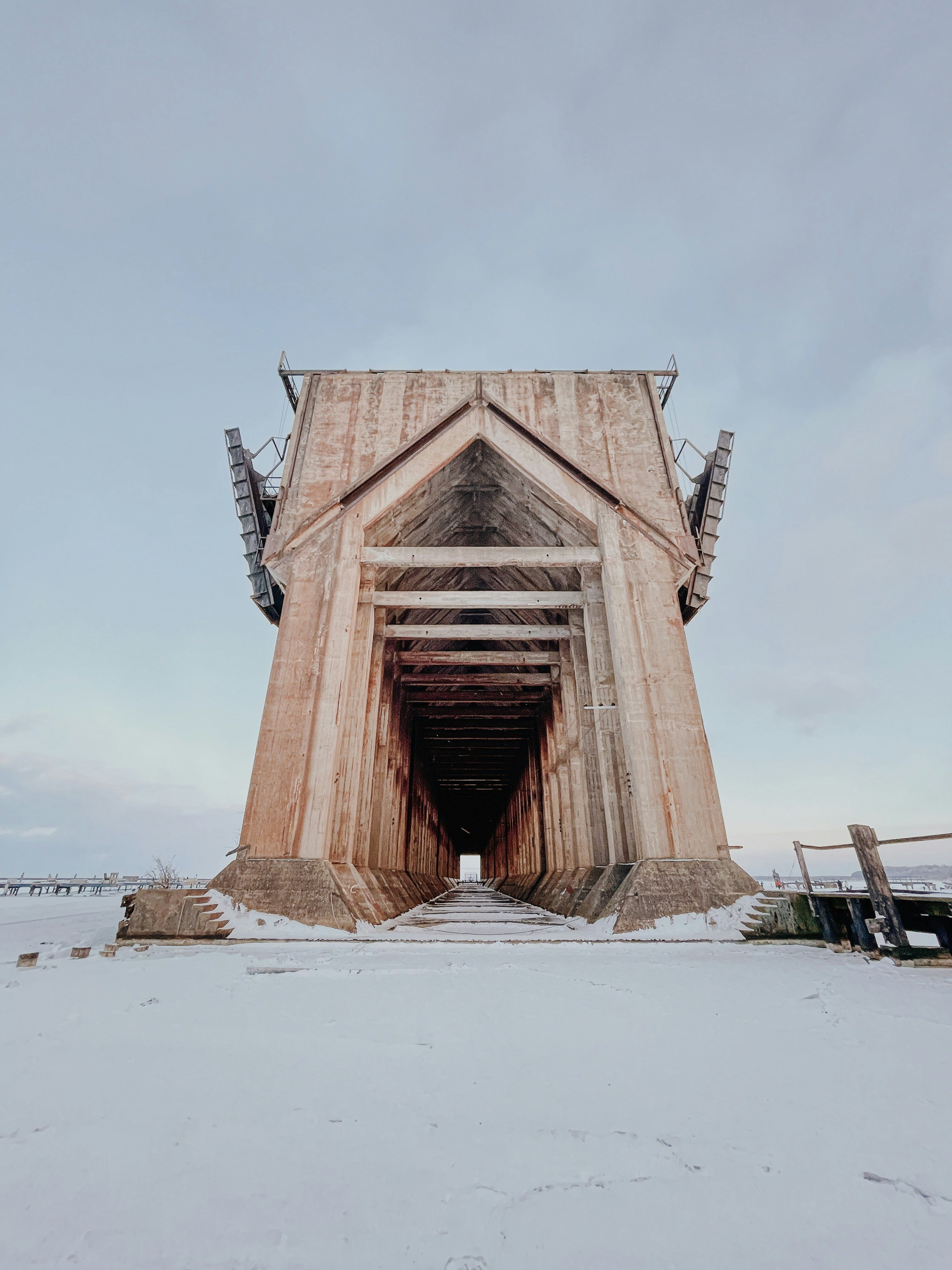 Massive concrete structure stands prominently against a pale sky, framed by snow-covered ground, evoking a sense of nostalgia for industrial architecture.