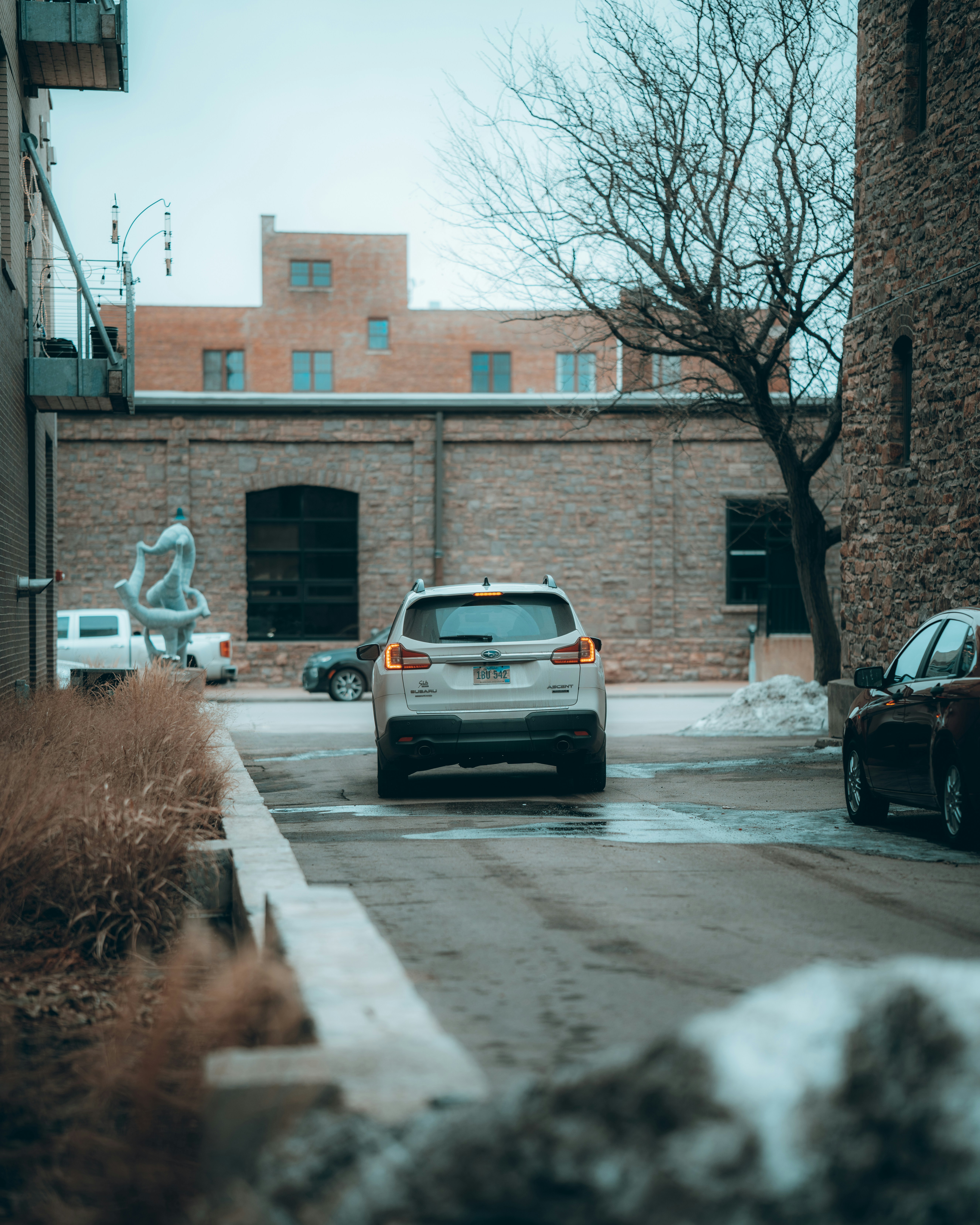 A white SUV parked in a narrow alleyway, framed by textured stone buildings and a hint of modern art in the background. The scene captures the calmness of urban life.
