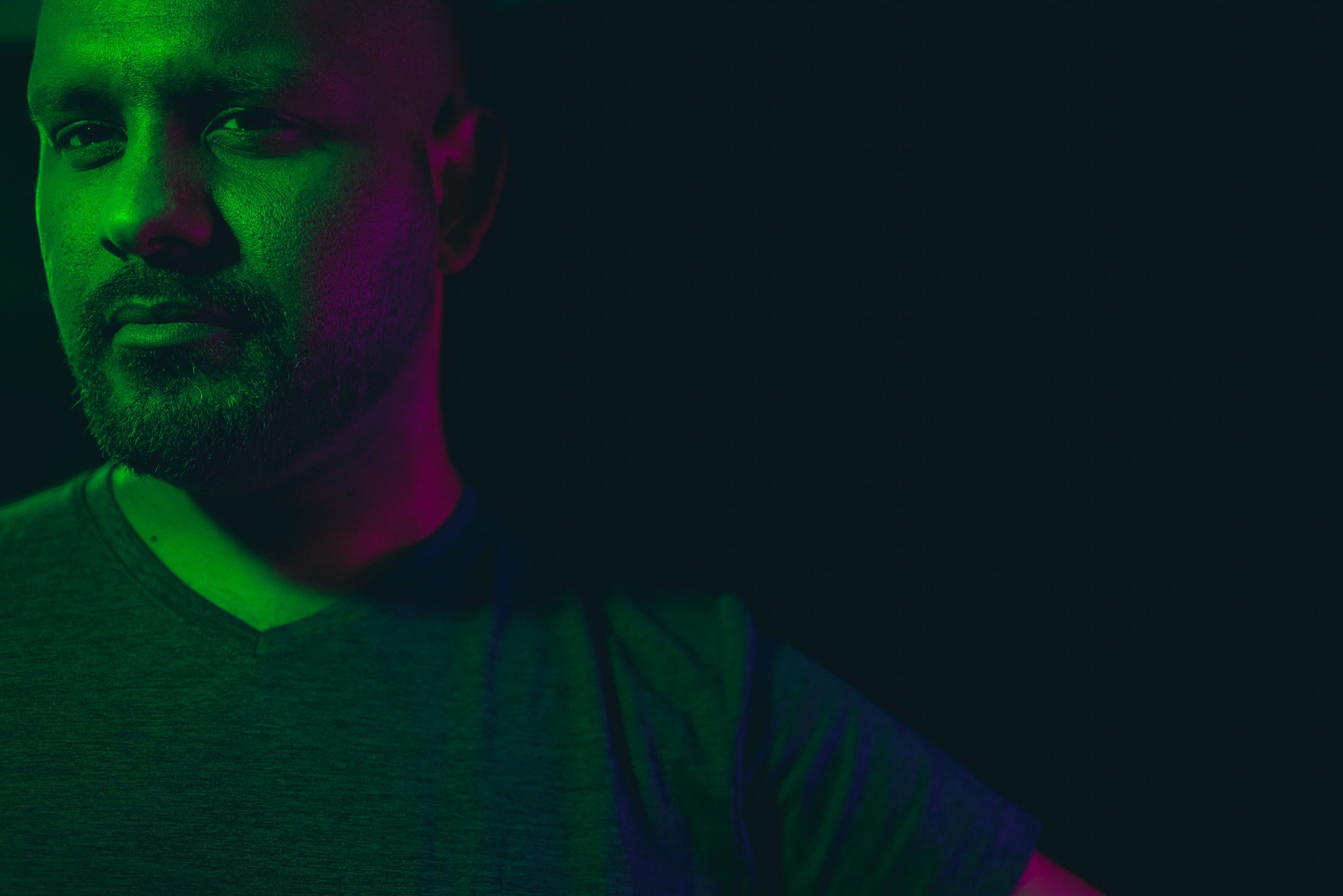 Man's face partially illuminated with green and magenta lighting against a dark background.