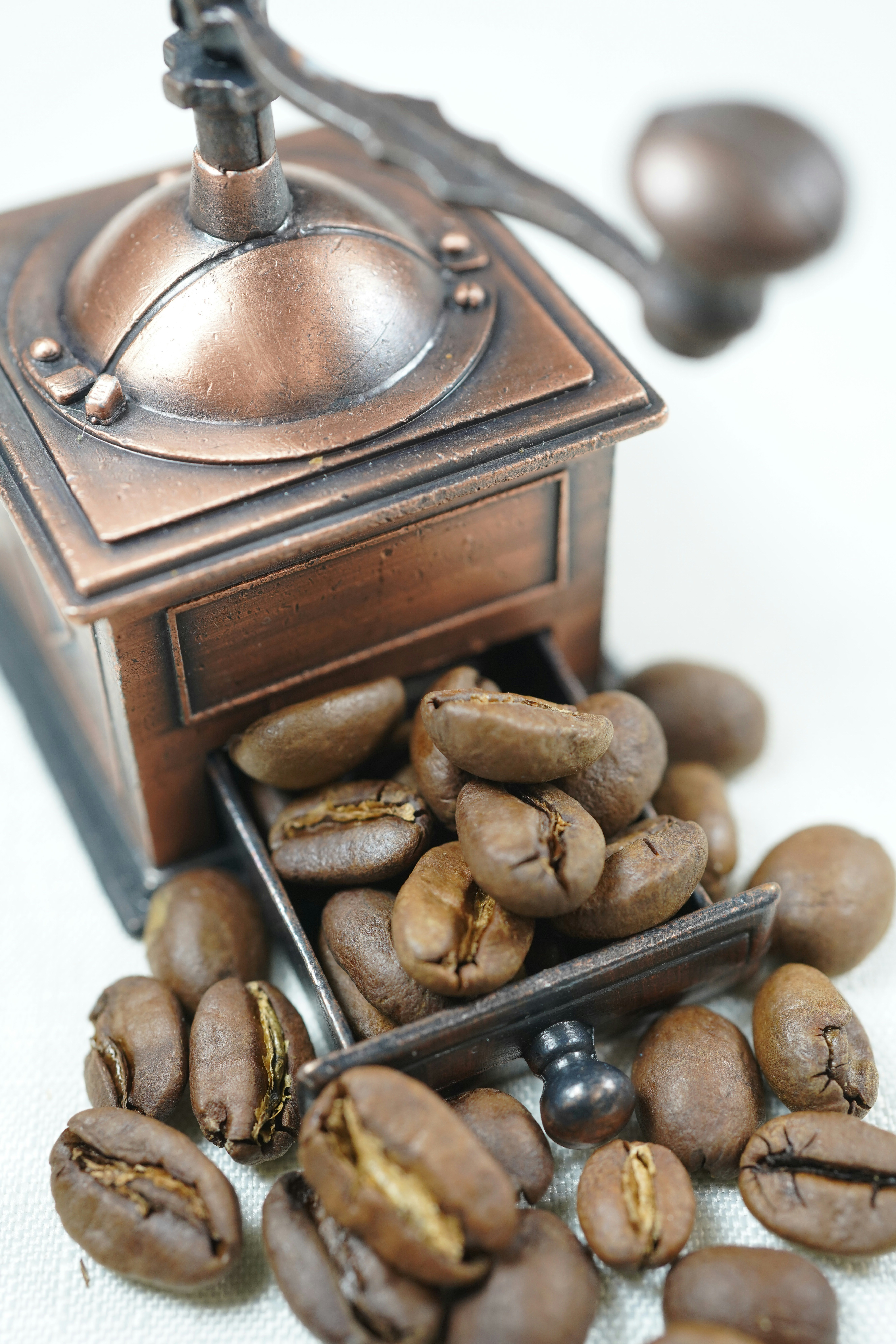 Antique coffee grinder with beans spilling from its drawer, showcasing the beauty of coffee preparation.