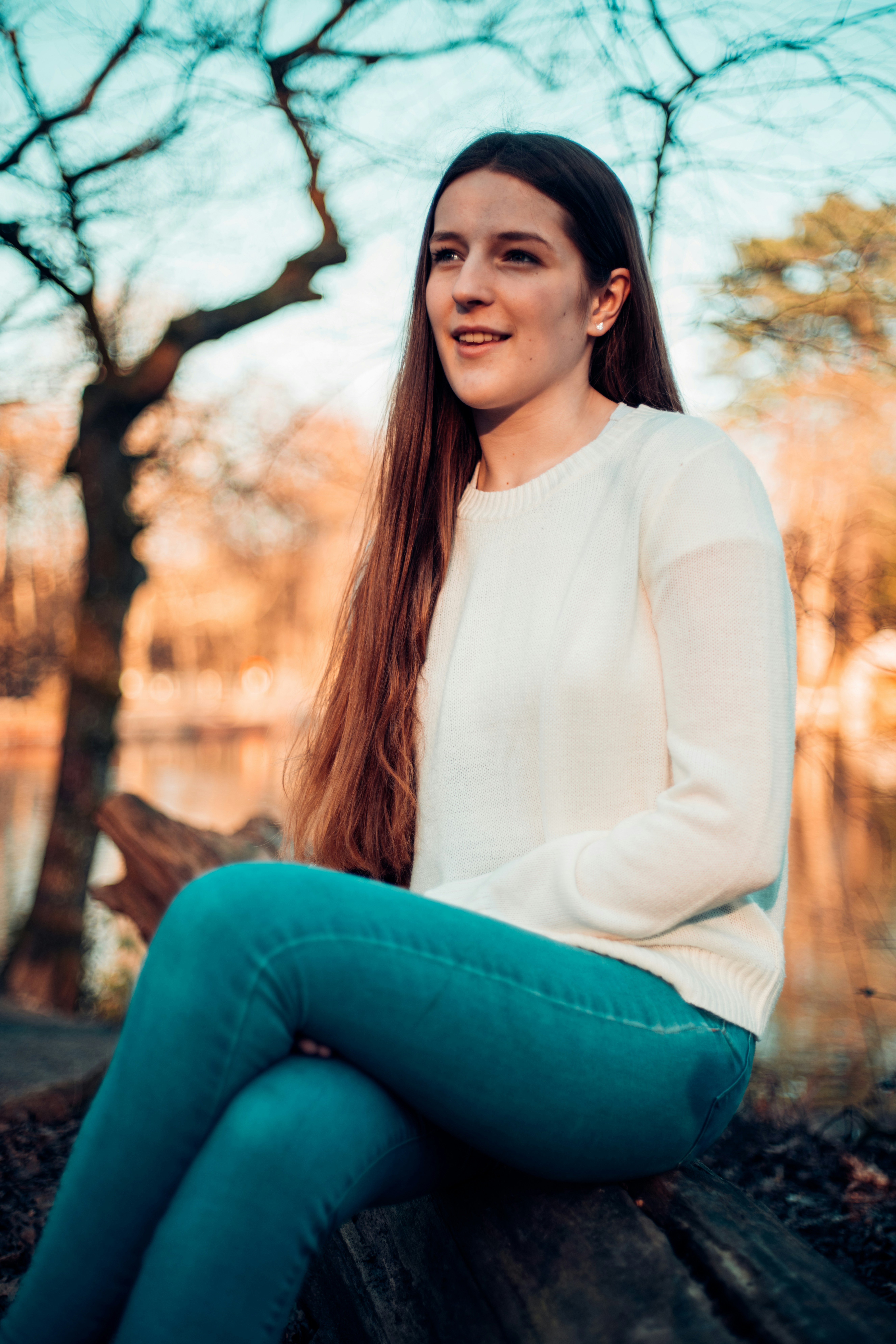 woman in white long sleeve shirt and blue denim jeans sitting on brown wooden bench during