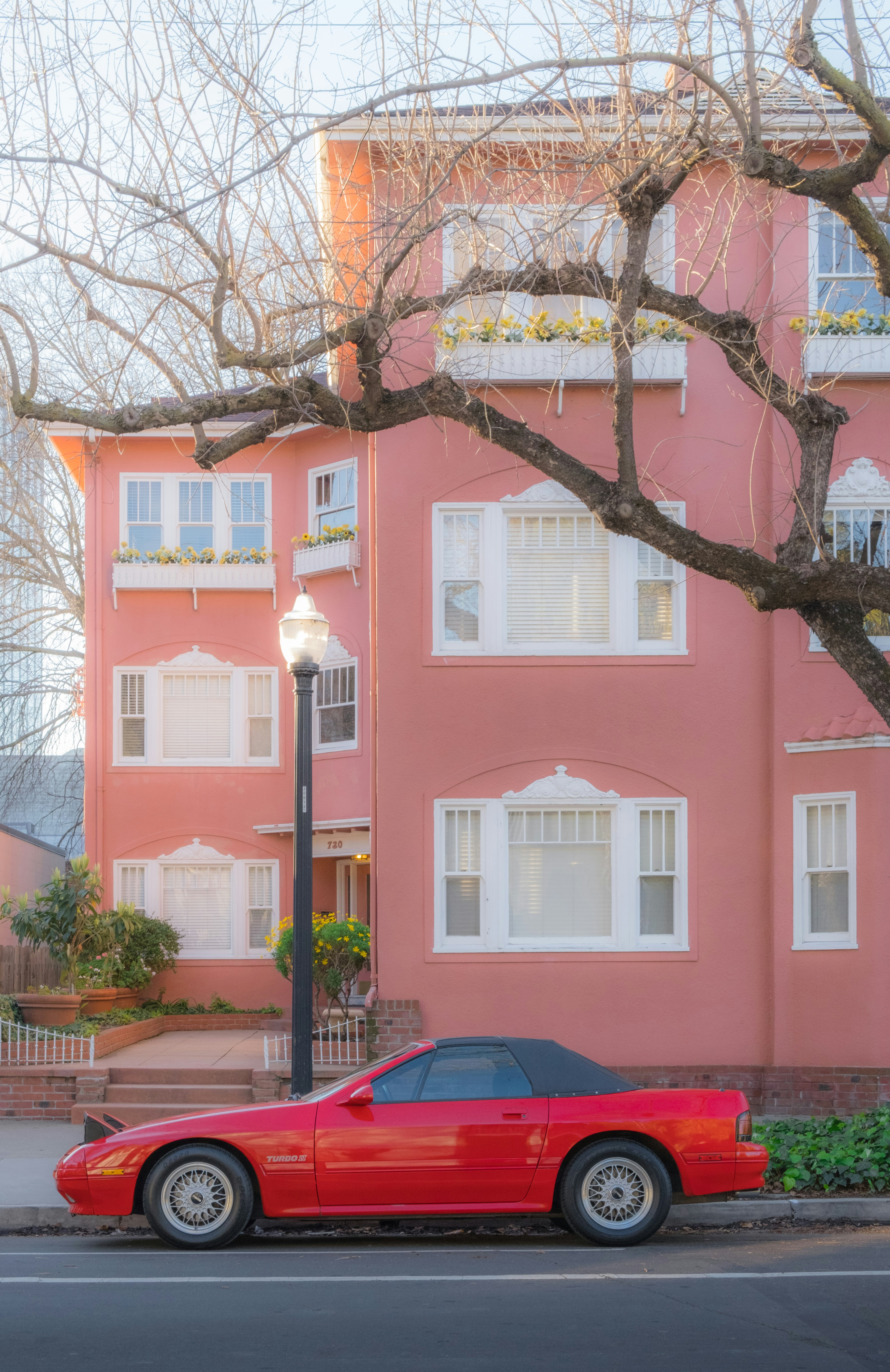Red Convertible at a Pink Apartment Building, Framed by Bare Branches