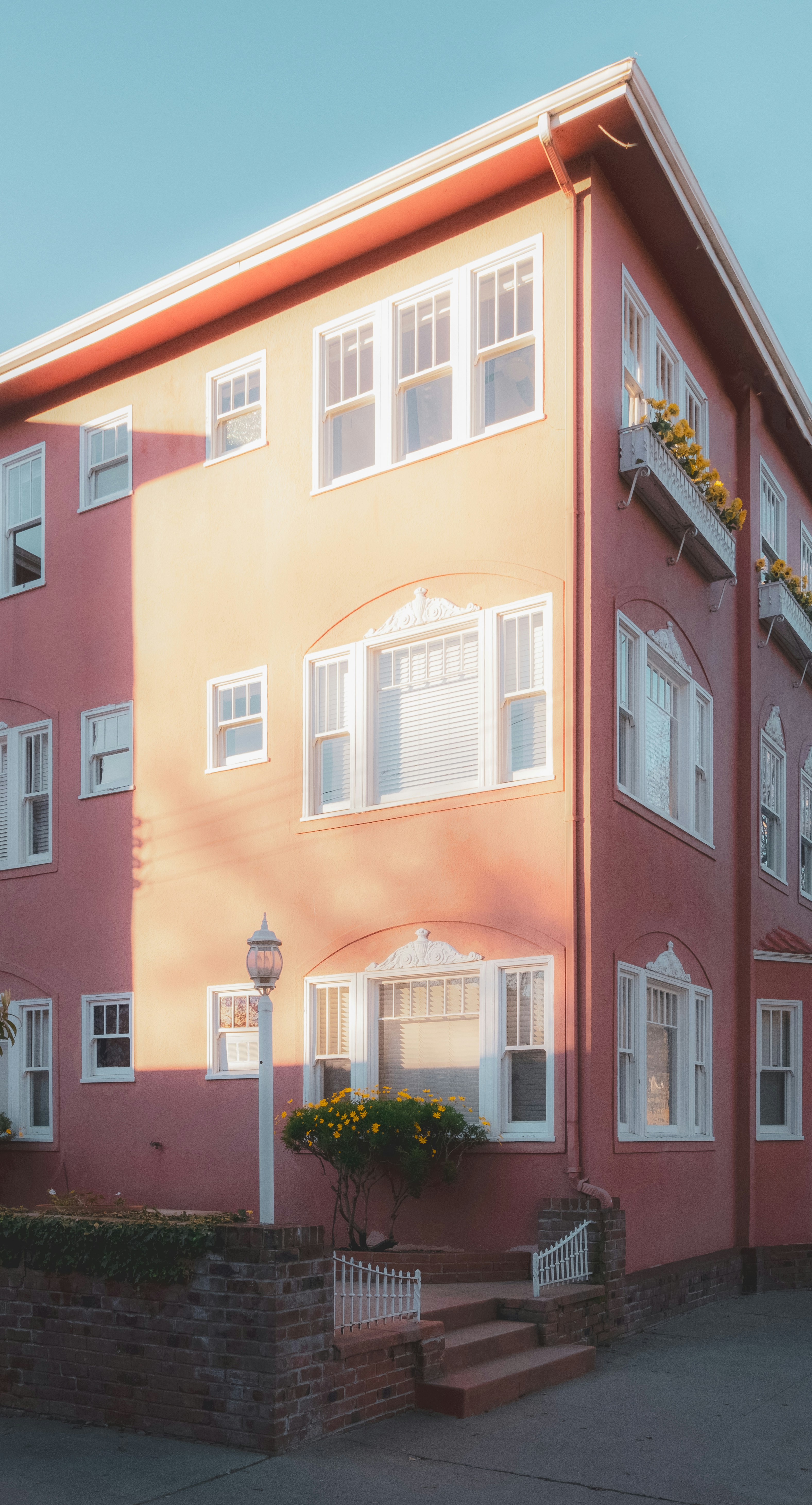 A vibrant coral-colored apartment building featuring elegant architectural details and blooming flowers in window boxes. Soft afternoon light casts warm shadows on the facade.