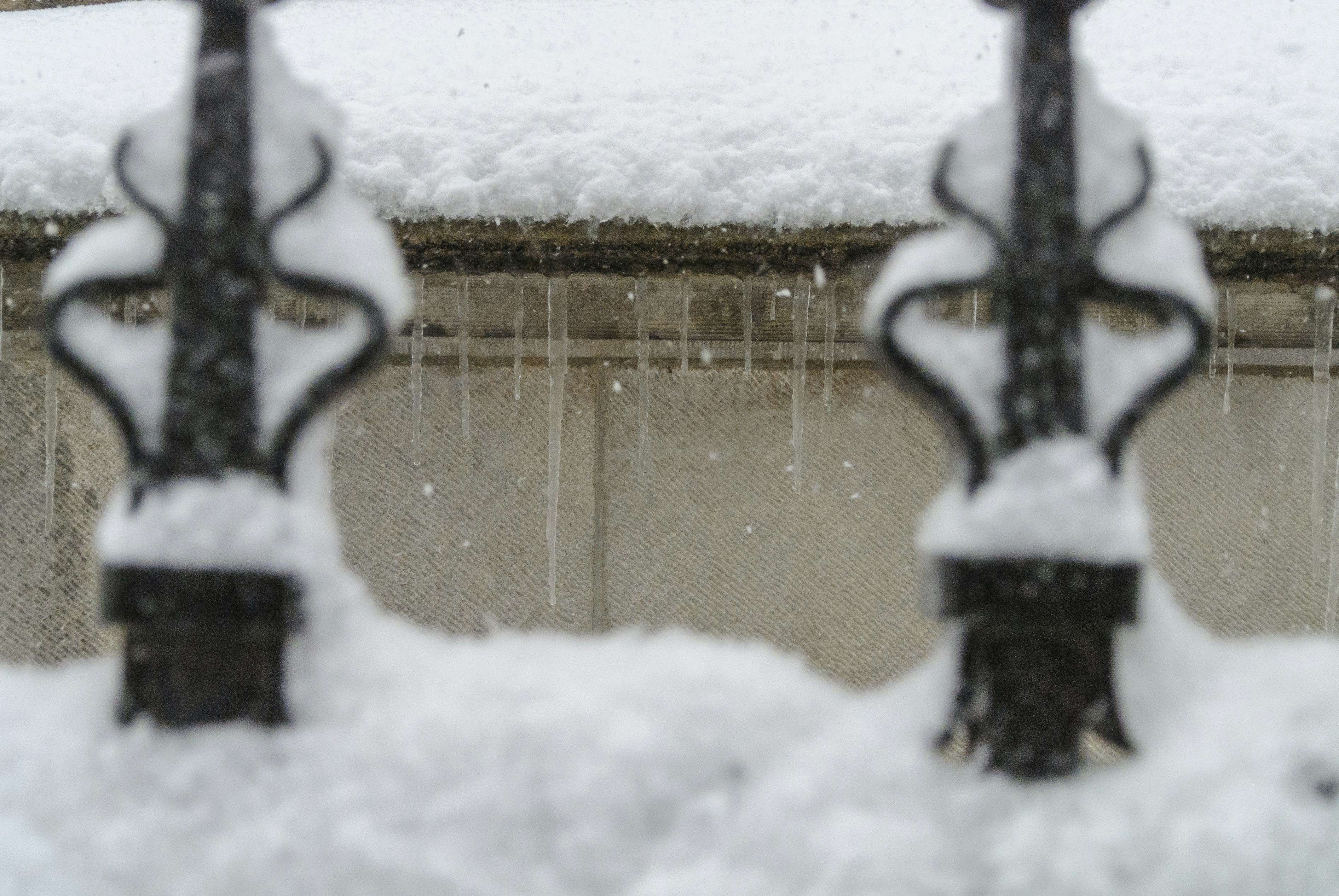Snow-dusted decorative iron railing frames a wall with dripping icicles in the background.