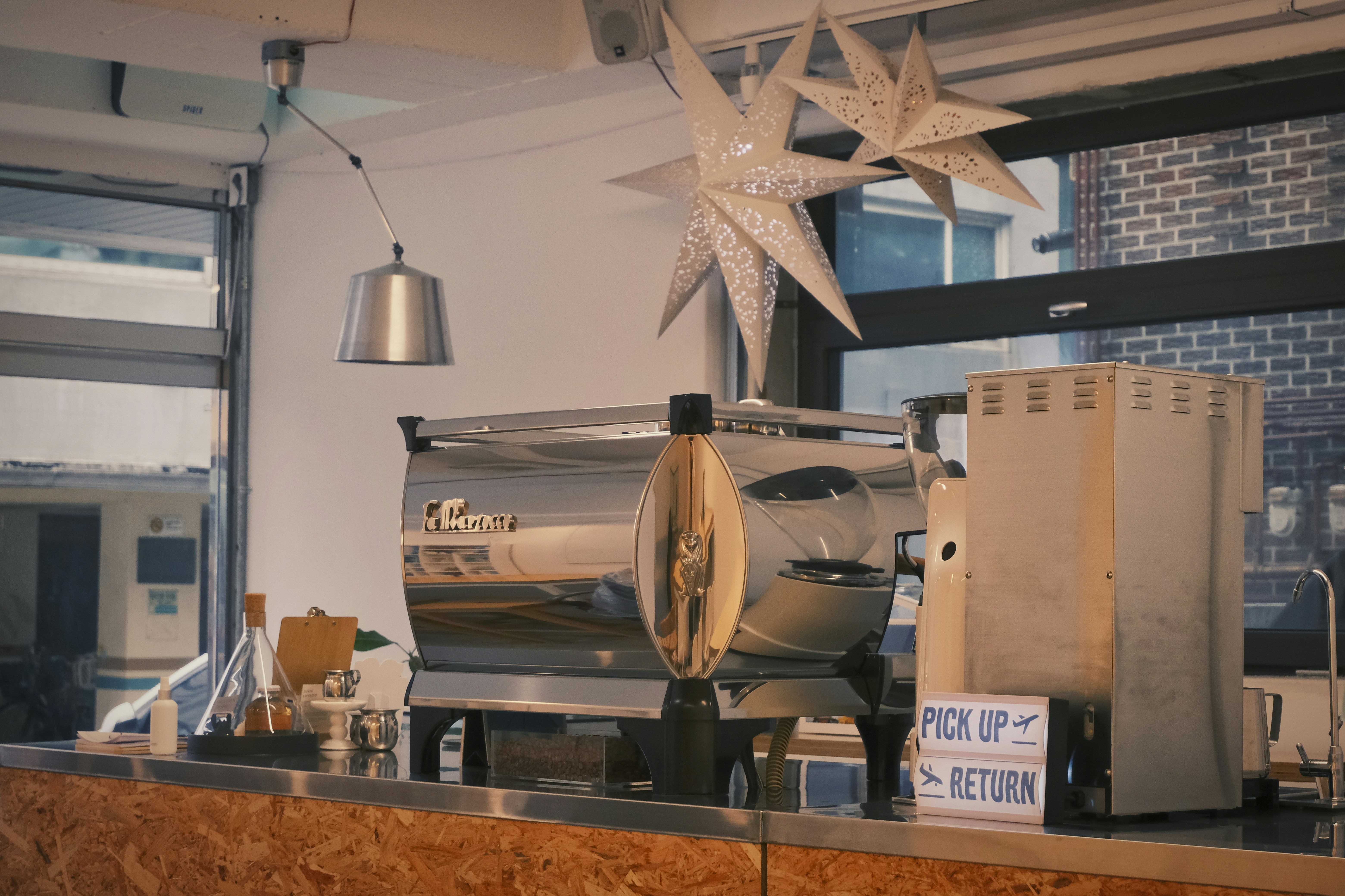 Metal coffee roaster and equipment under star-shaped decorations in a modern café setting.