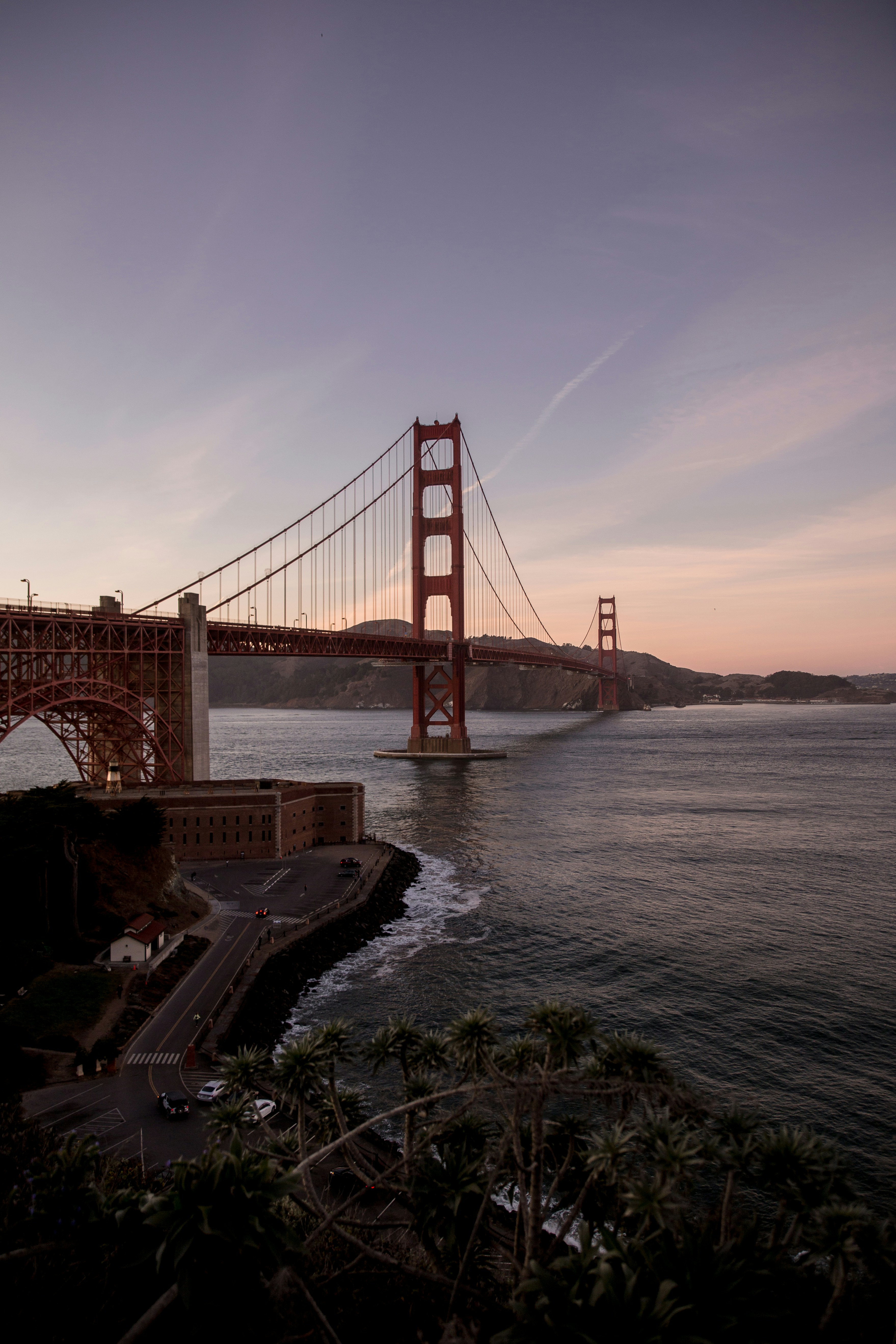 Golden Gate Bridge silhouetted against a twilight sky, with waves gently lapping at the shore below.