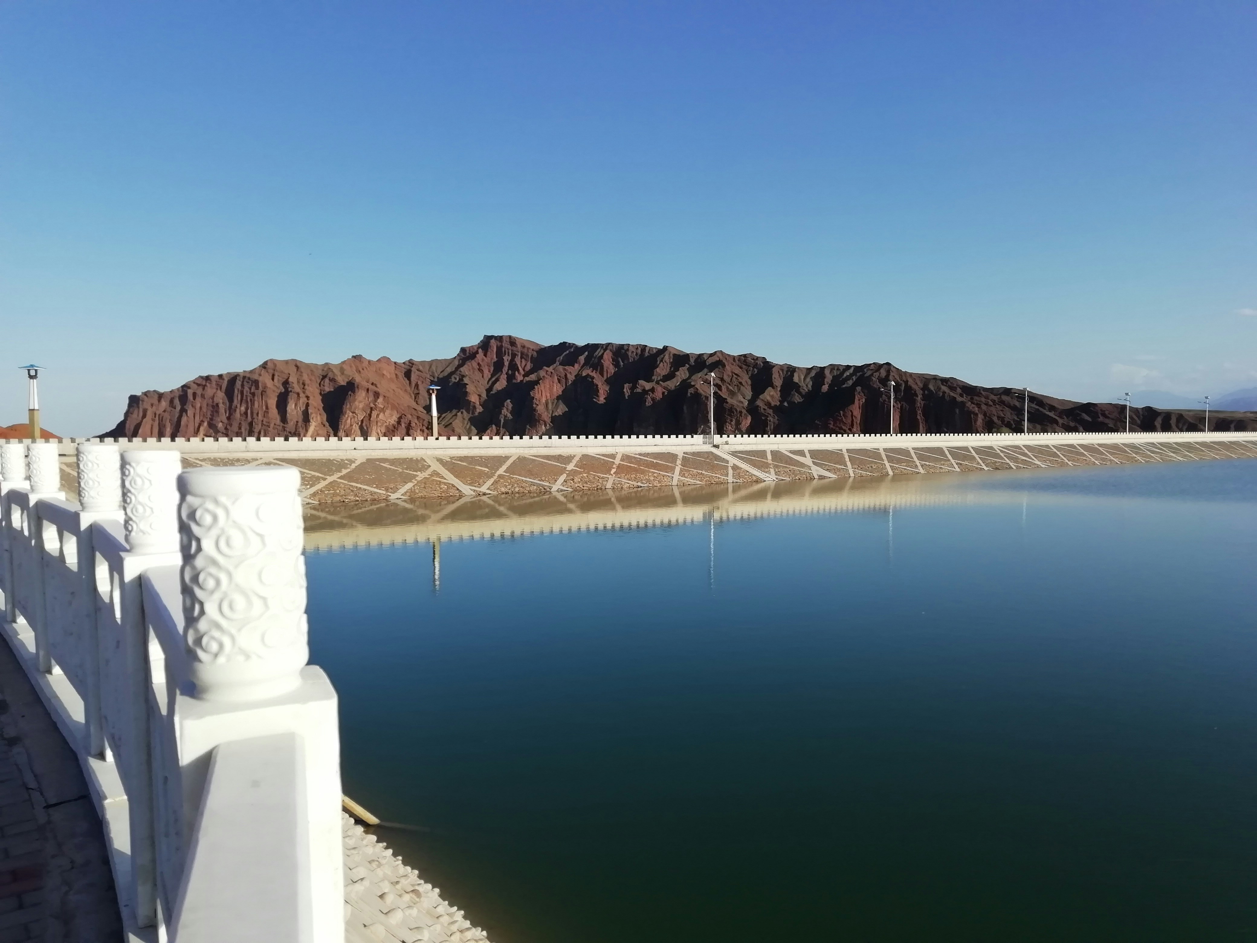 A tranquil lakeside view featuring a rocky mountain backdrop and a white railing along the water's edge.