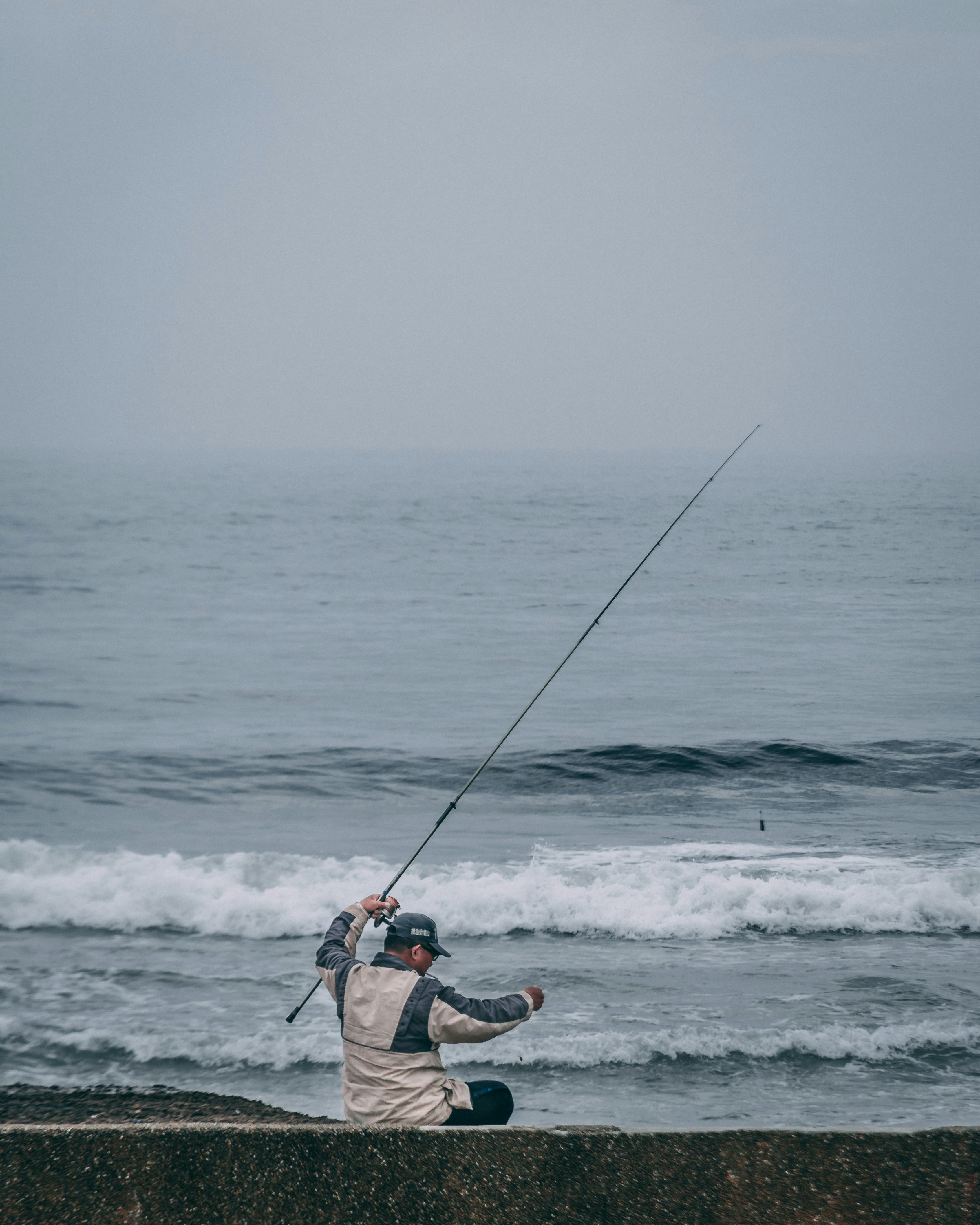 Man in red and black jacket and black pants fishing on sea during ...