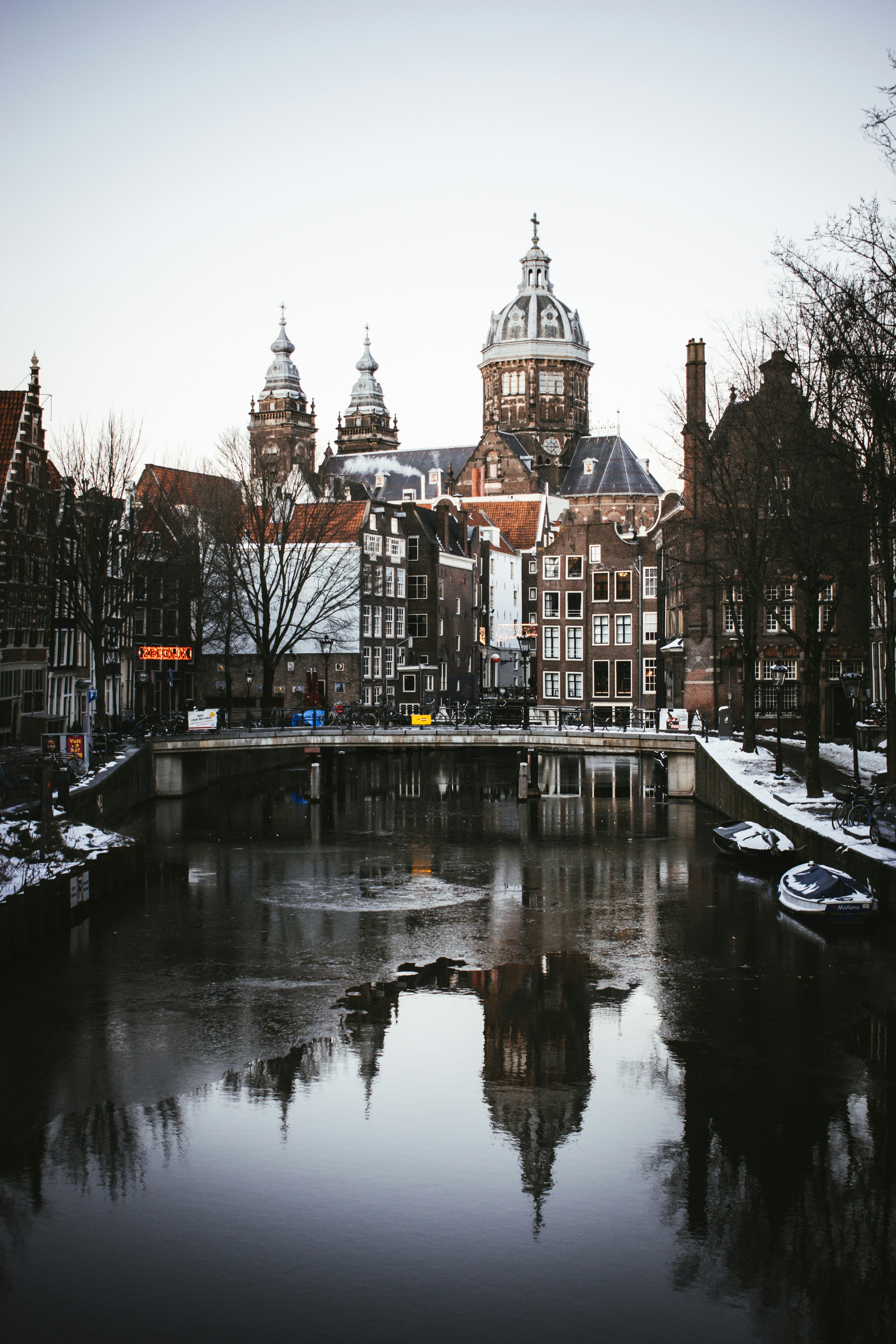Historic Amsterdam buildings reflecting in a calm canal, framed by bare trees and a soft winter light.