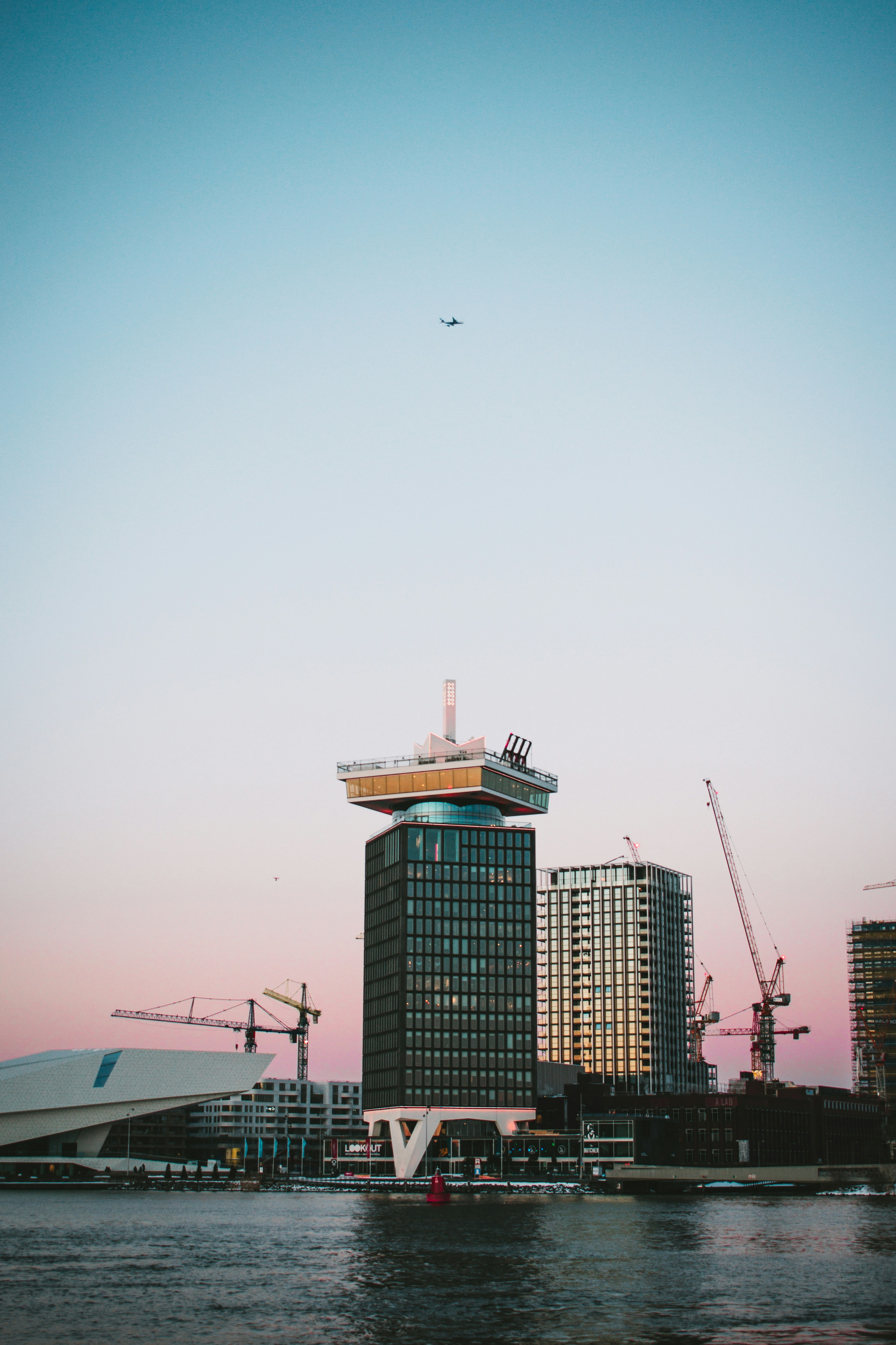Airplane soaring above urban skyline with pink and blue gradient sky at dusk.