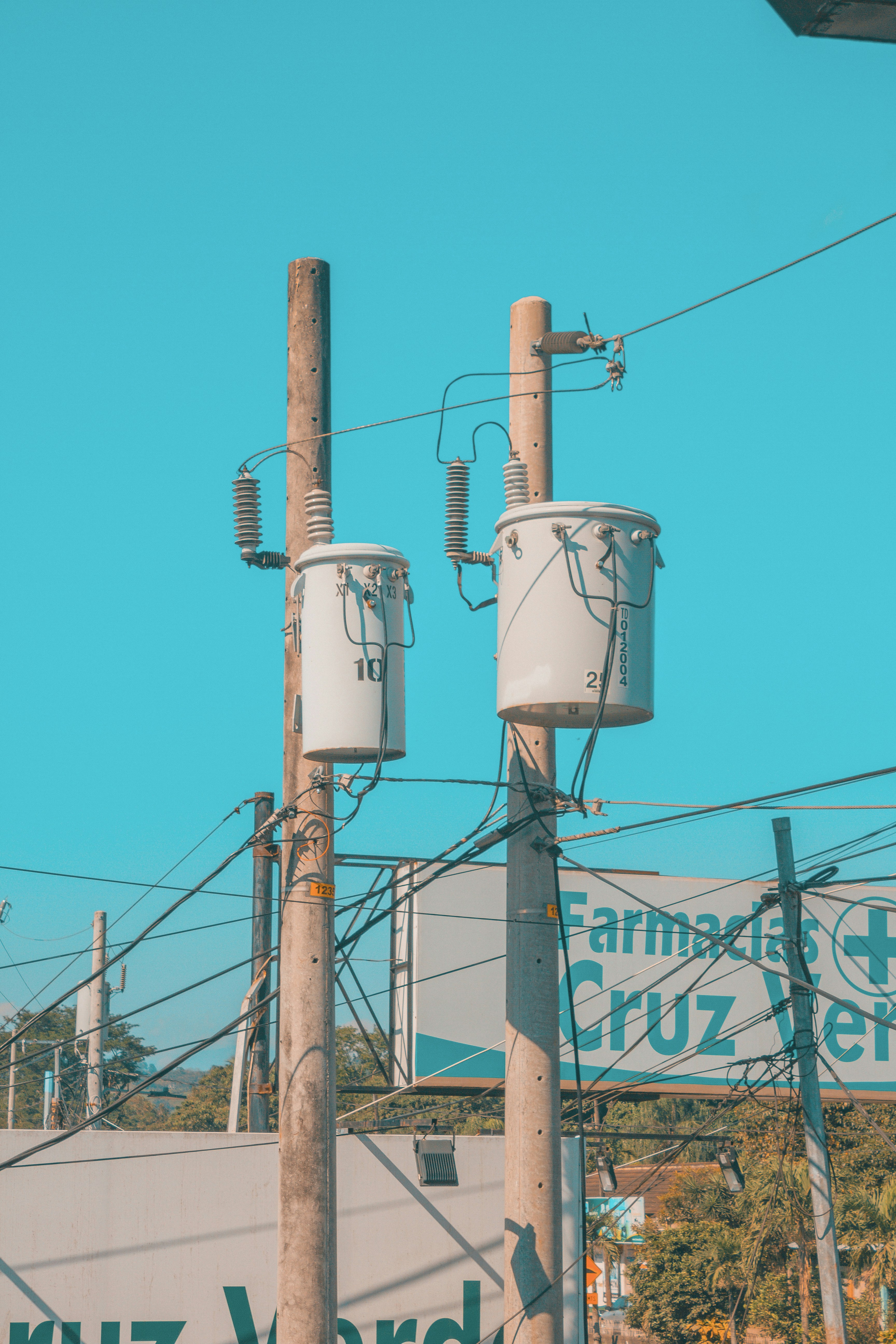 Blue Sky Voltage: Transformer Poles Against a Cyan Canvas