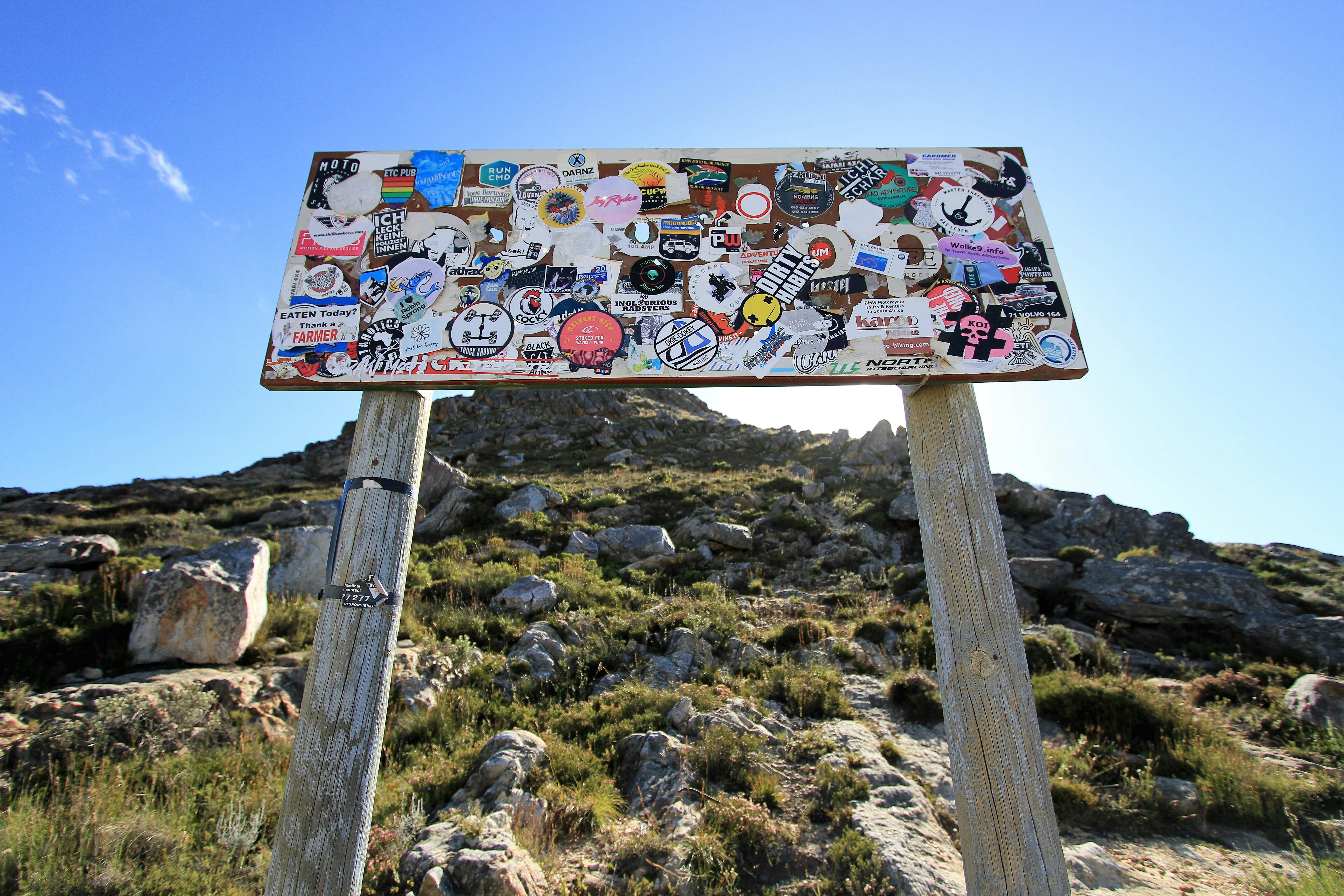 Colorful stickers plastered on a wooden signpost against a rocky hillside, showcasing a collage of expressions and messages.