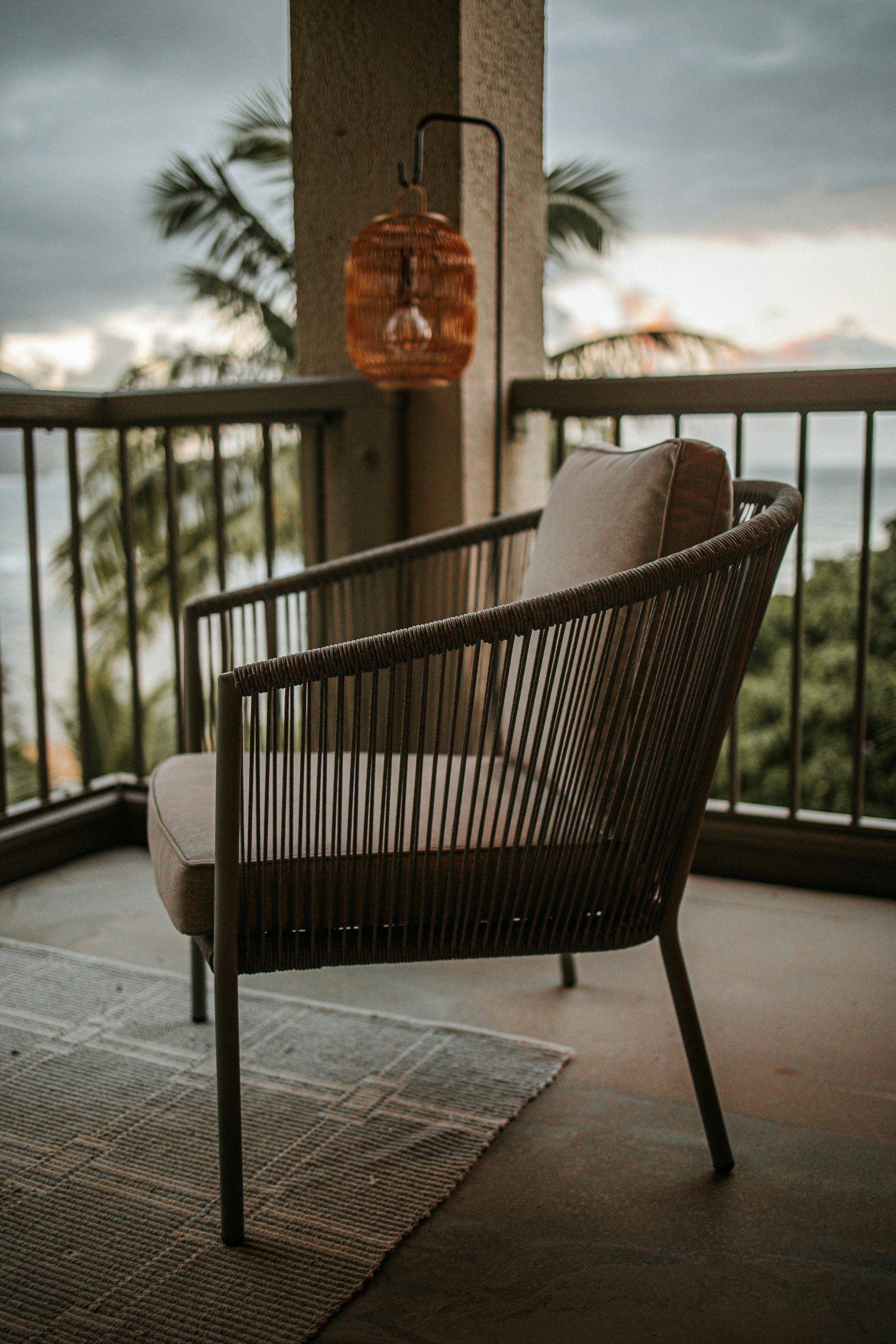 Stylish outdoor chair positioned on a balcony, accompanied by a woven pendant light and lush greenery in the background.