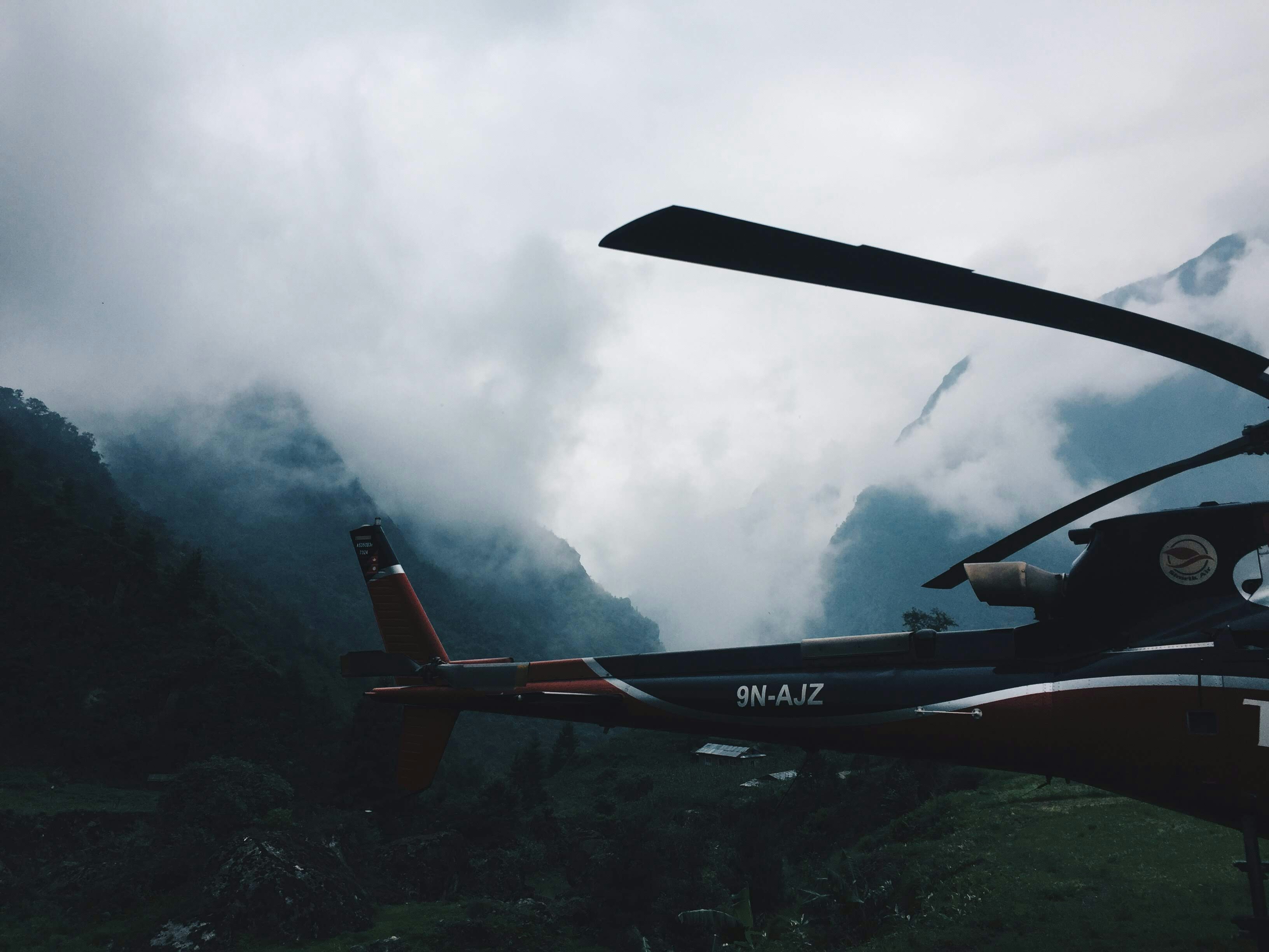 Red helicopter slicing through a fog-blanketed valley