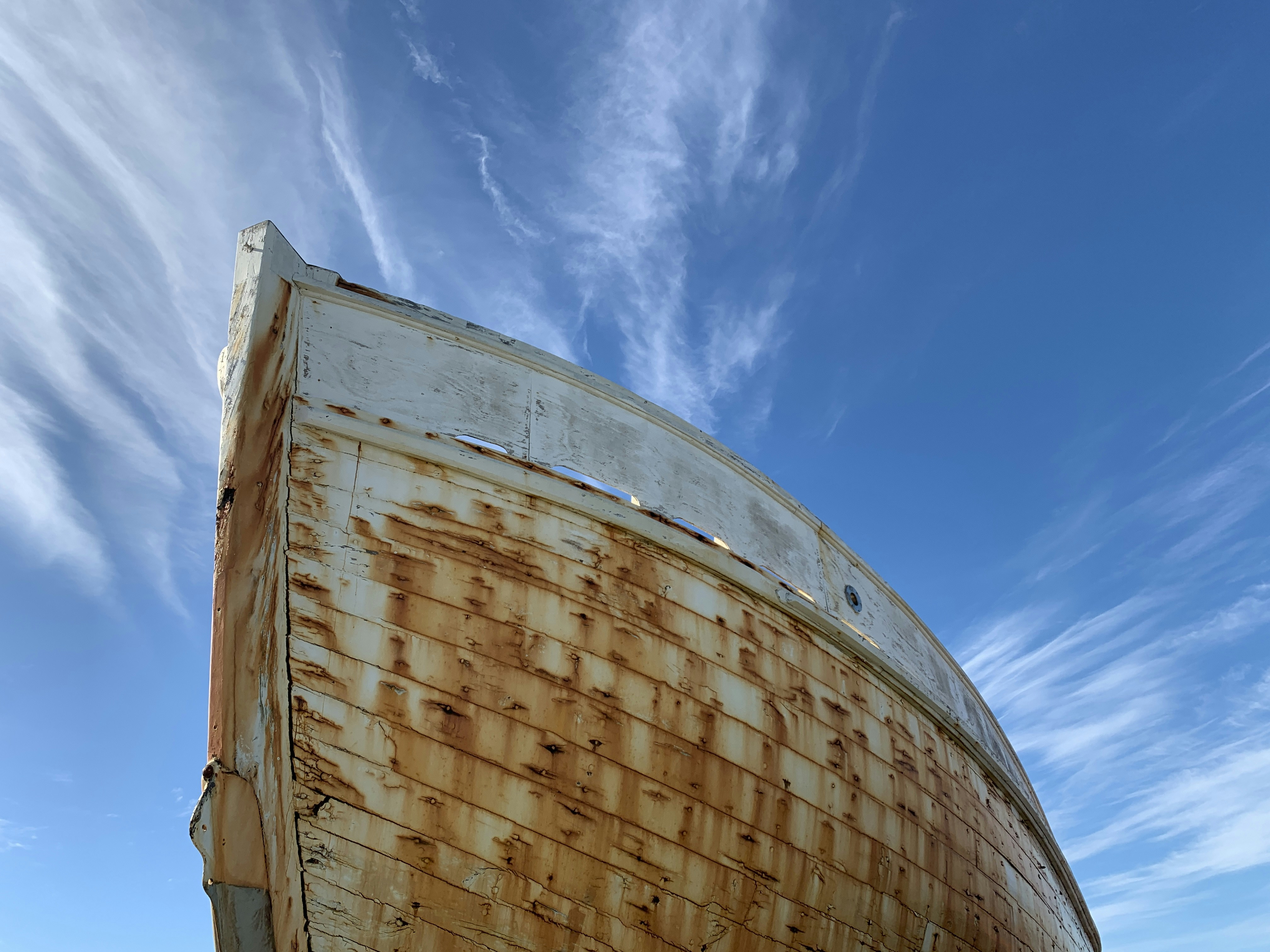 Rusty ship hull set against a vibrant blue sky with swirling clouds.