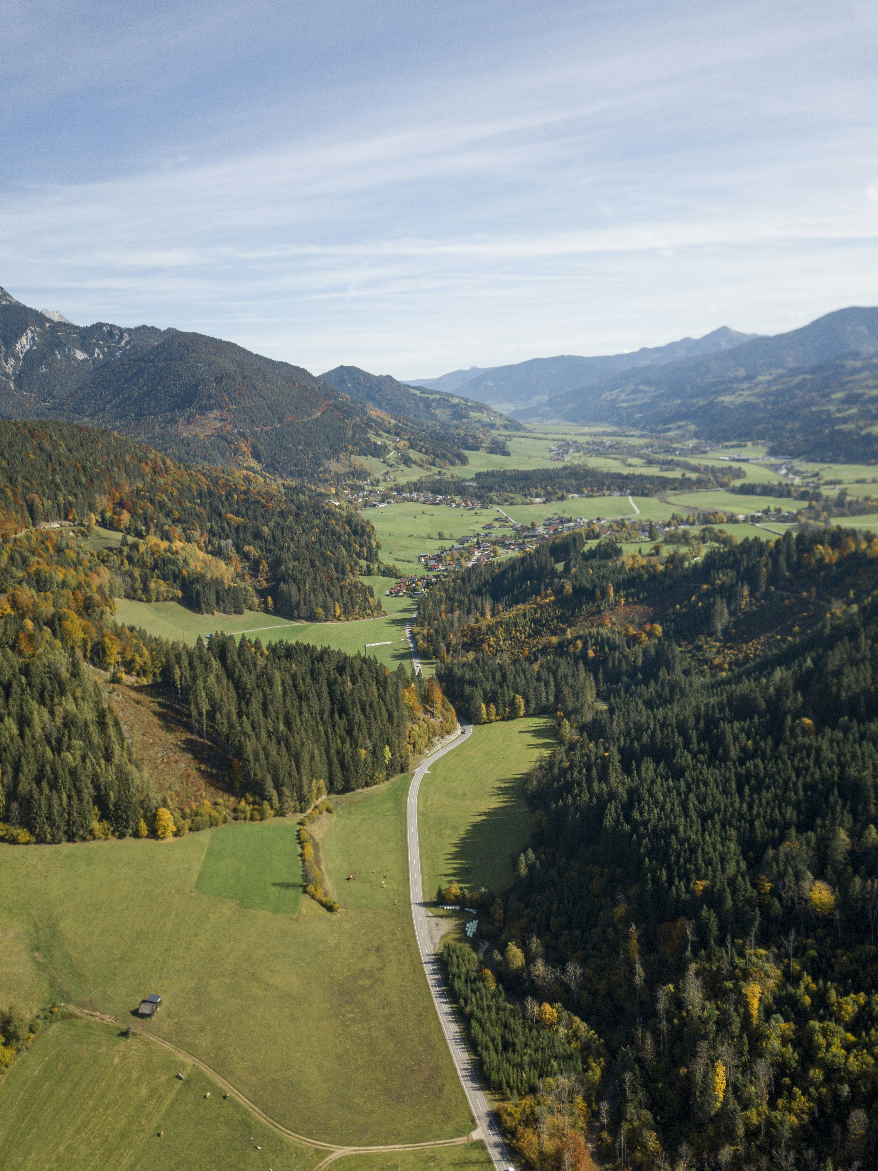 Vast green fields and rolling hills adorned with autumn foliage create a picturesque valley scene. A winding road leads through the landscape under a clear blue sky.