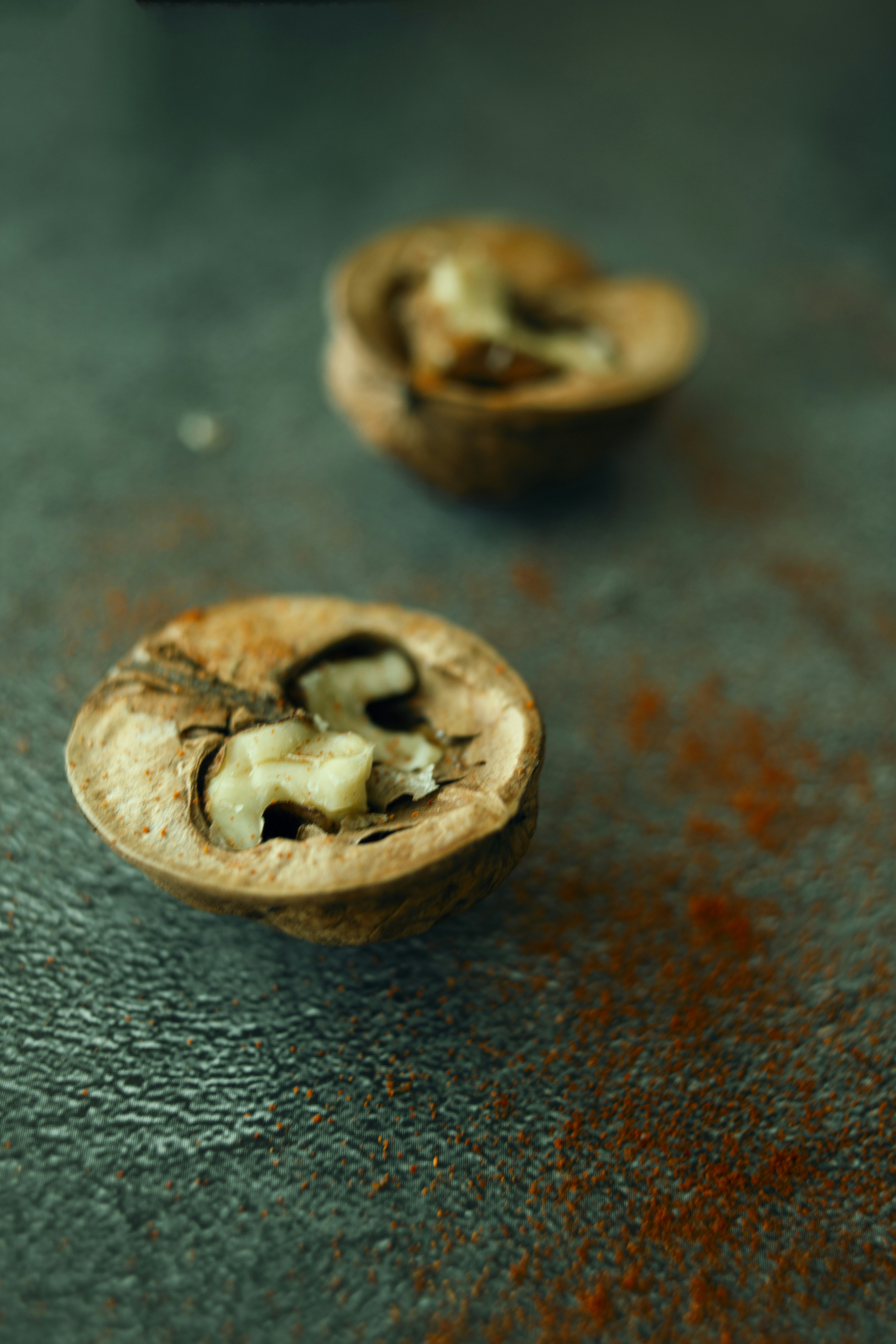 Close-up of a cracked walnut shell revealing its creamy interior, set against a textured surface with hints of spice. 