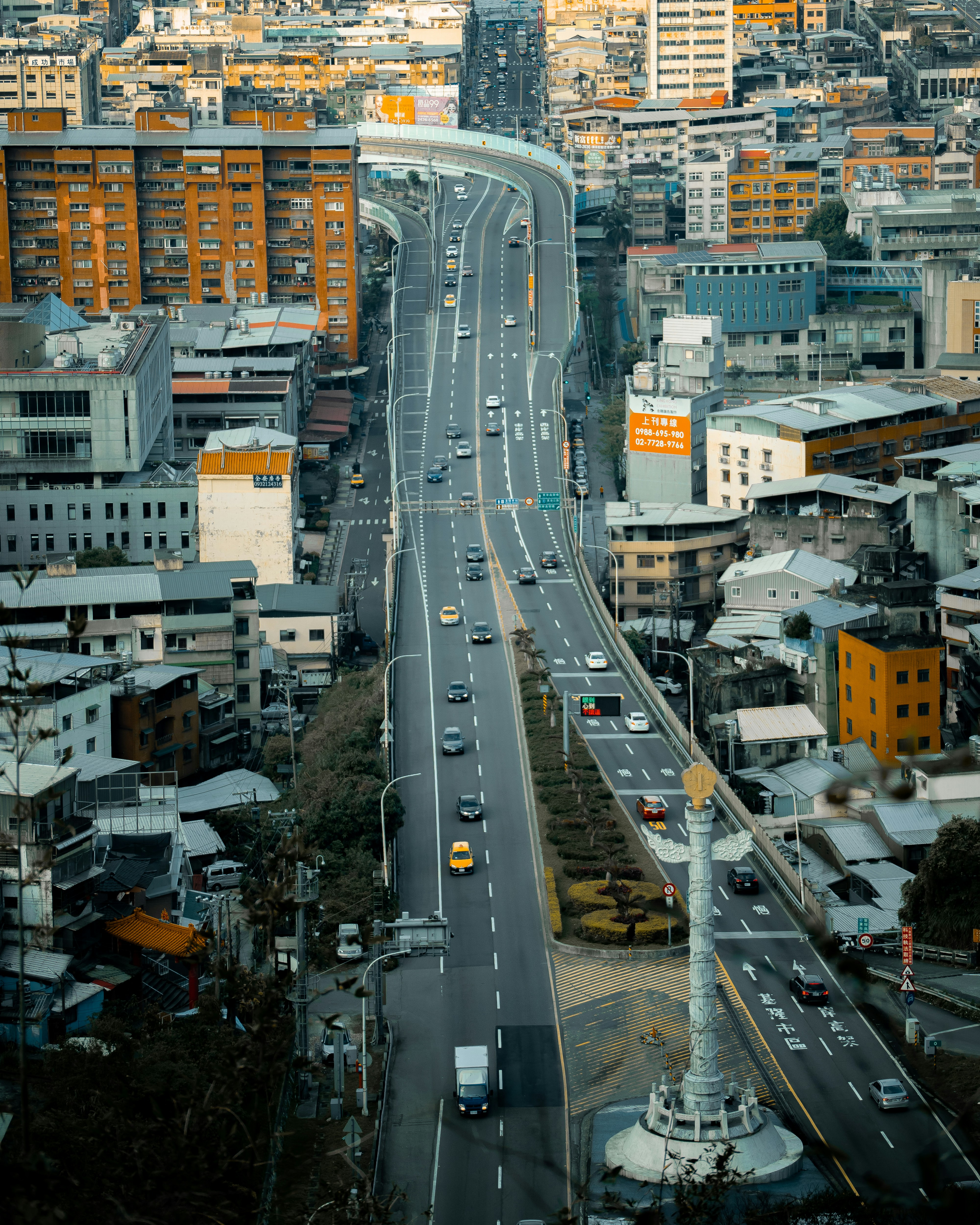 Aerial view of a busy urban highway winding through a city, showcasing a mix of modern and traditional architecture. The scene captures the dynamic flow of traffic and urban life.