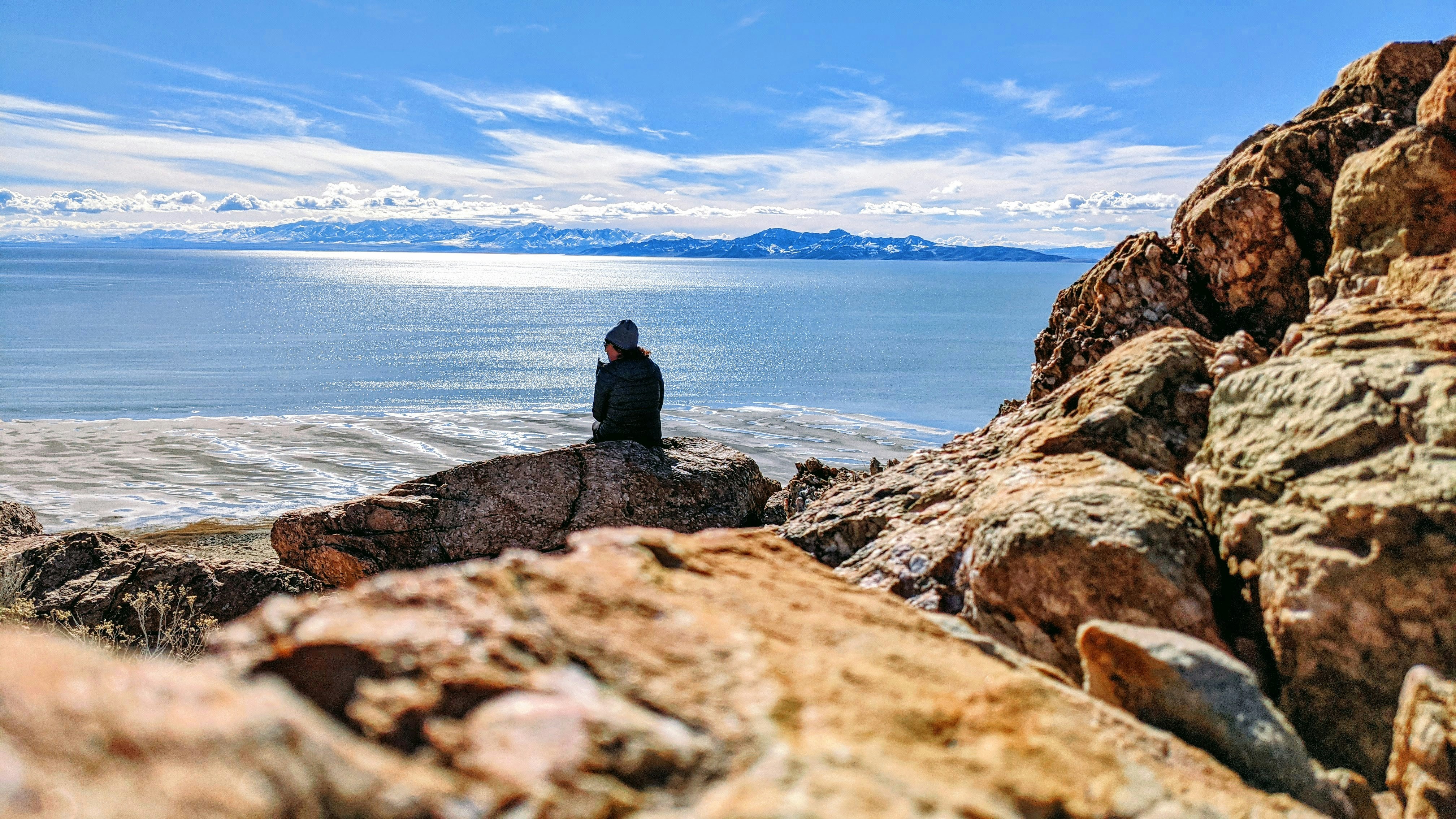 man in black jacket sitting on rock near sea during daytime