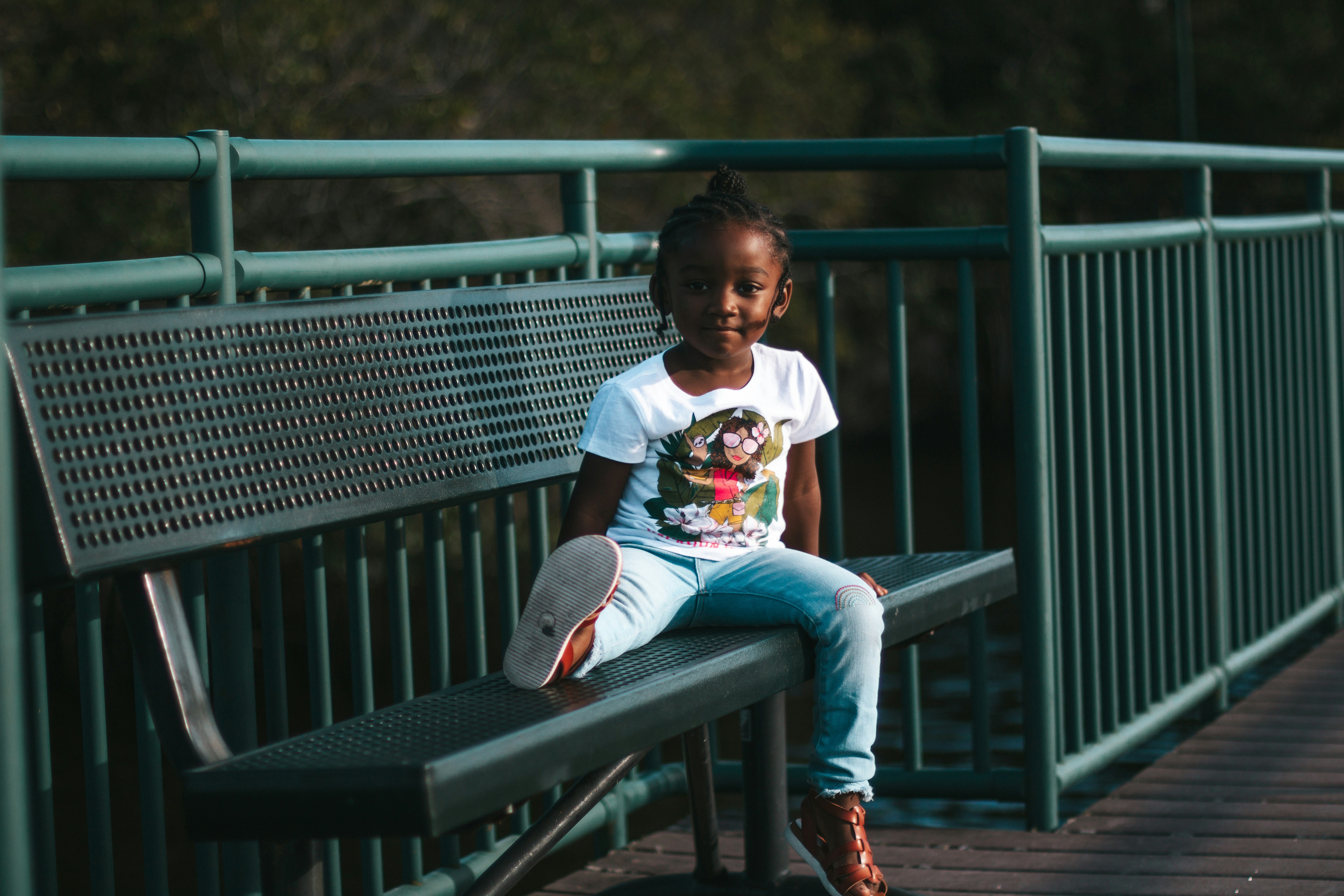 Young girl sitting on a park bench, wearing a colorful t-shirt and jeans, exuding a sense of happiness and playfulness.