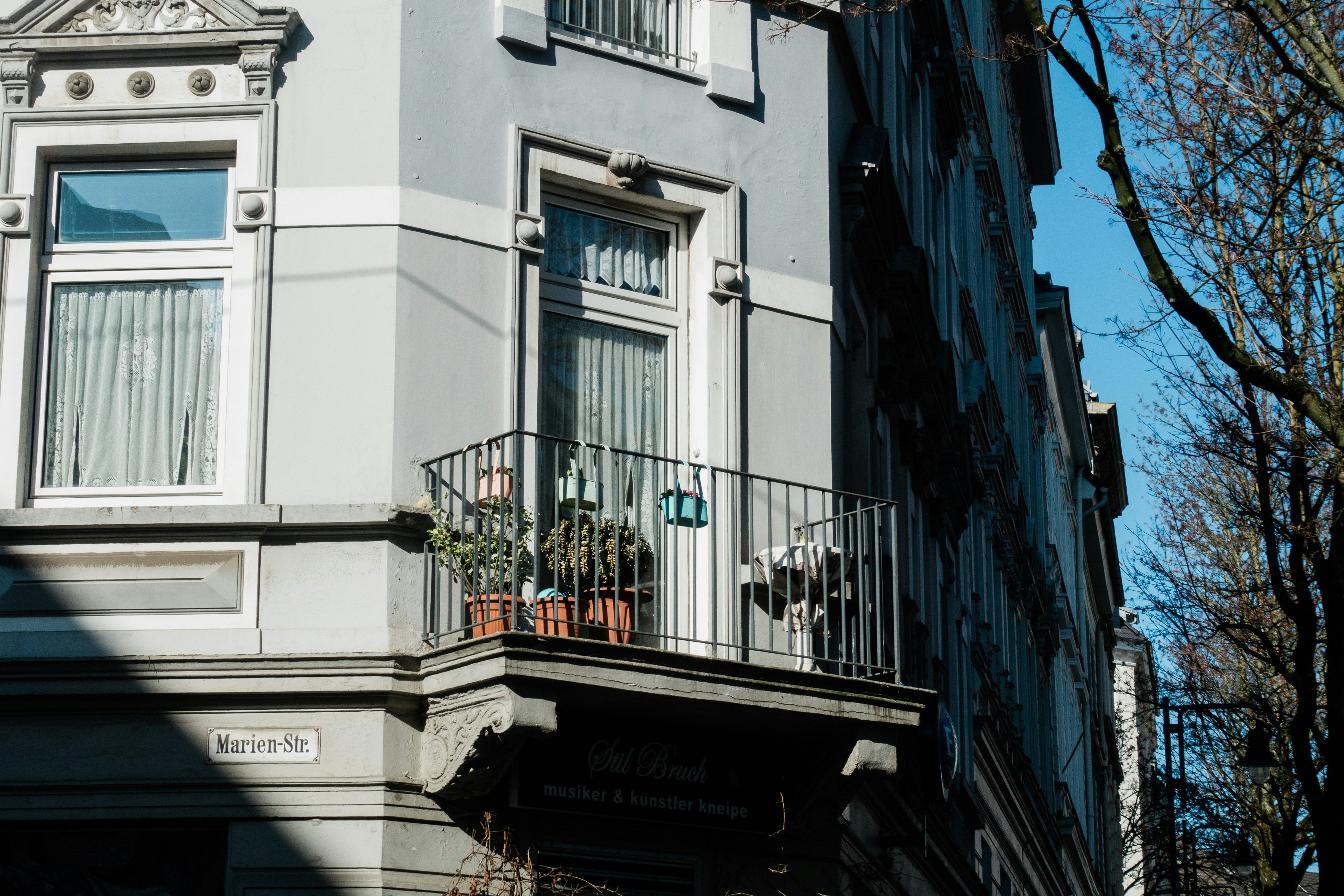 Corner balcony adorned with potted plants on a white concrete building under a clear blue sky.